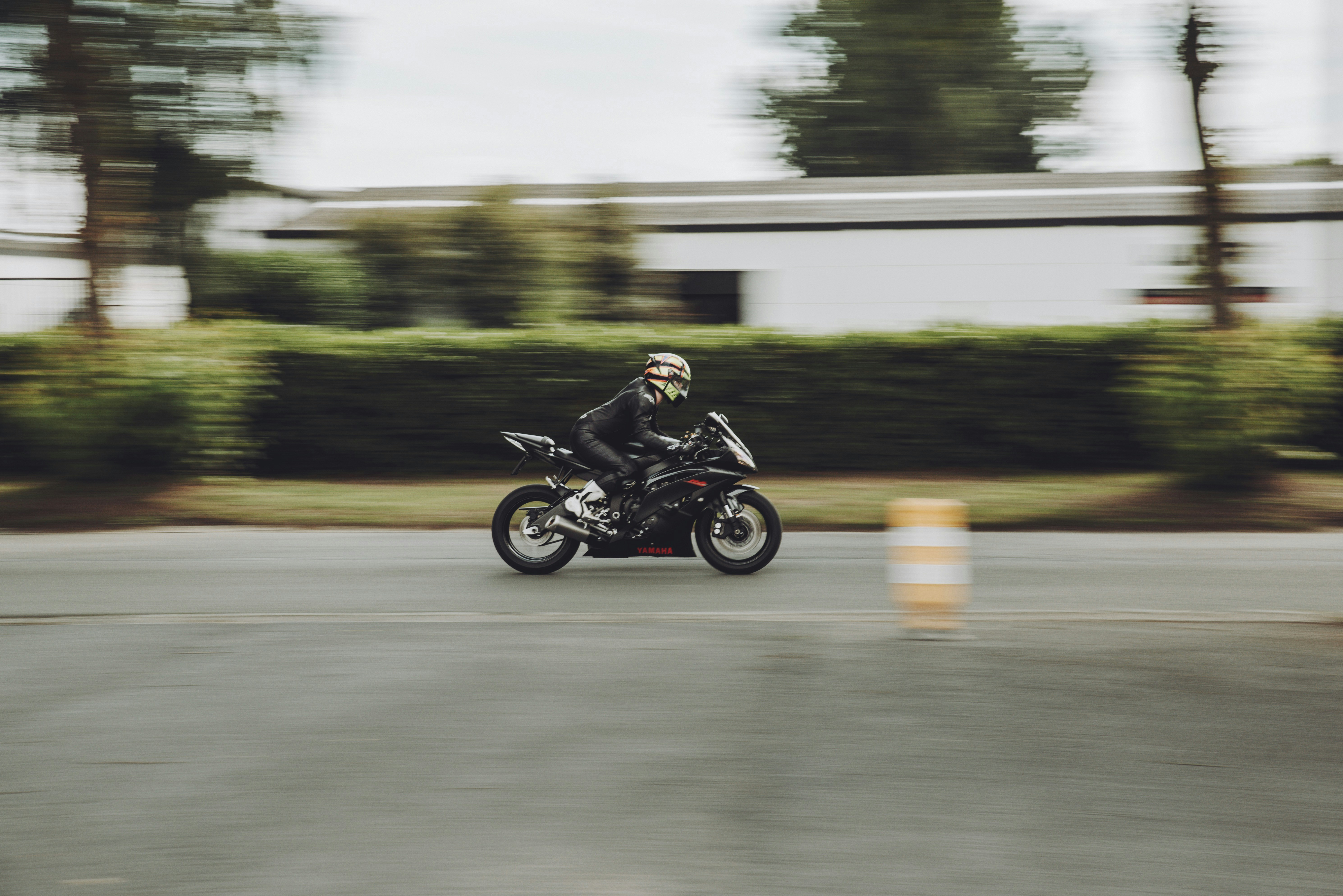 Motorcyclist racing past a blurred background of greenery and urban elements.