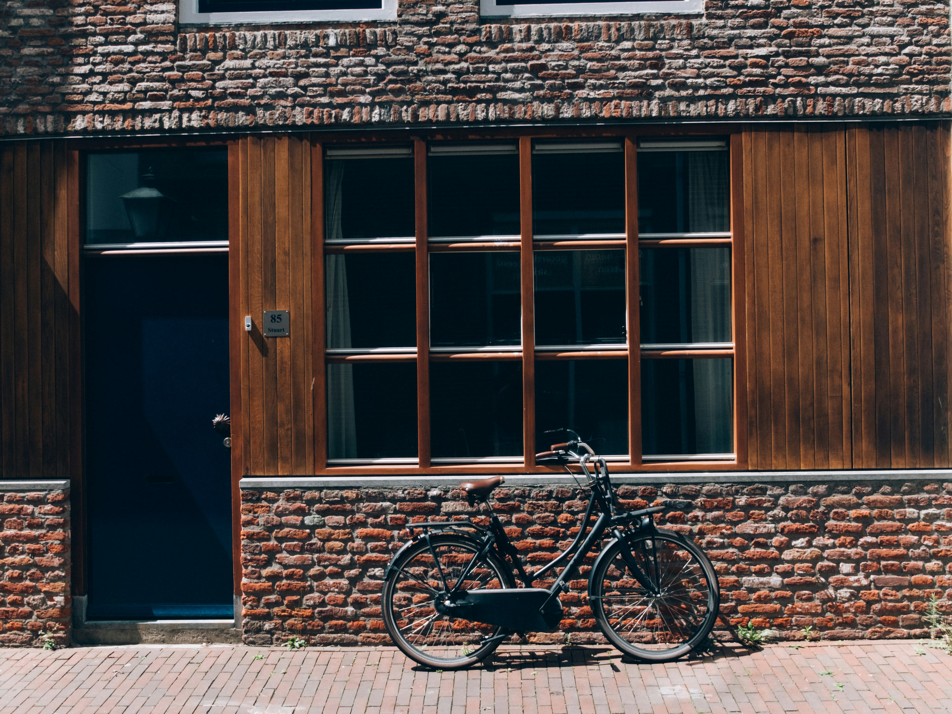 A sleek bicycle rests against a rustic brick wall, framed by large wooden windows that reflect the calm of the urban environment.