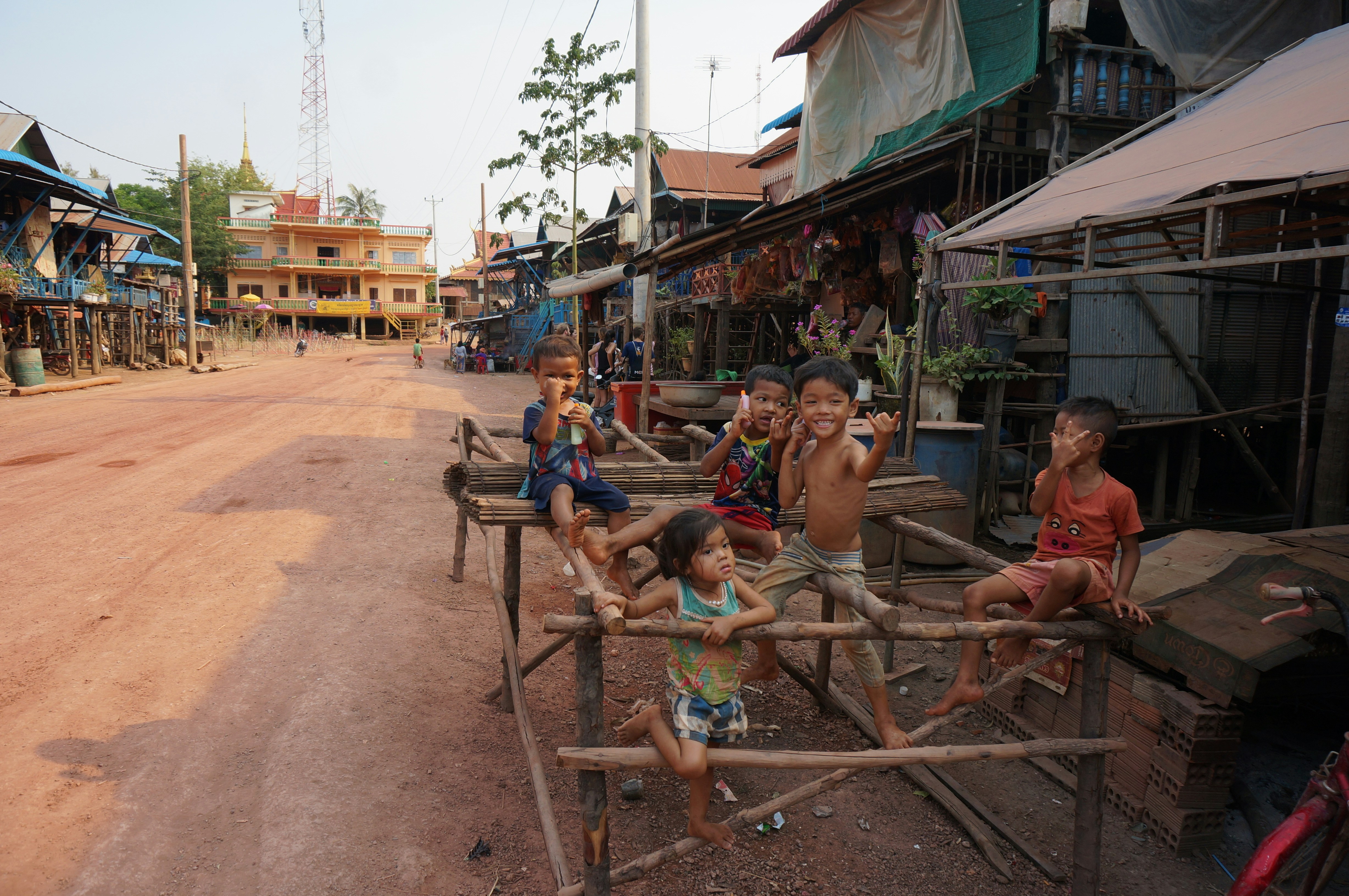 Children playing and smiling on makeshift wooden tables in a vibrant street setting in Cambodia.