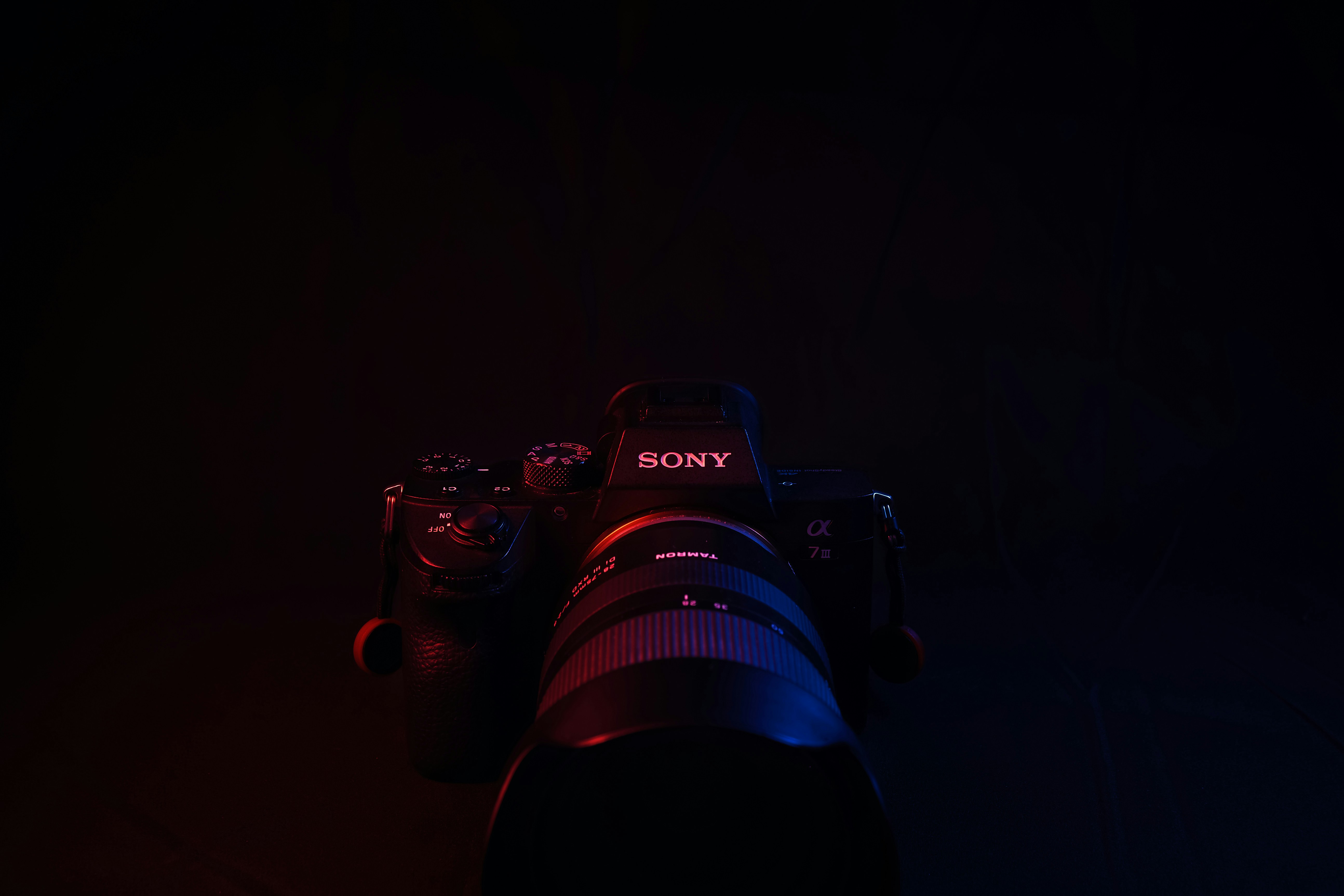 Sony Alpha 6000 camera positioned centrally against a dark backdrop, illuminated with subtle red and blue lighting.