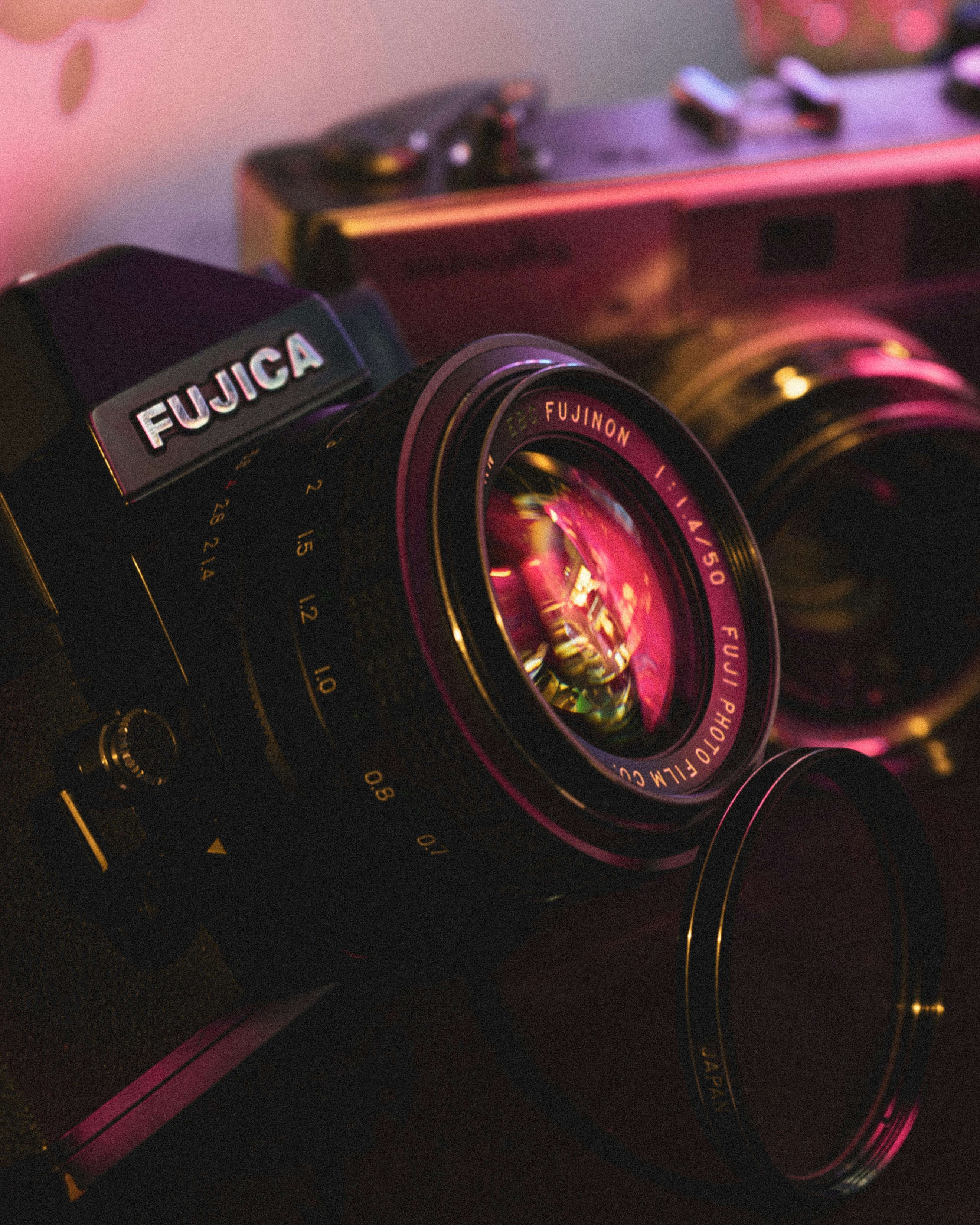 Close-up of a Fujica camera with vibrant lens reflections, highlighting its classic design and intricate details. The background features additional vintage cameras.