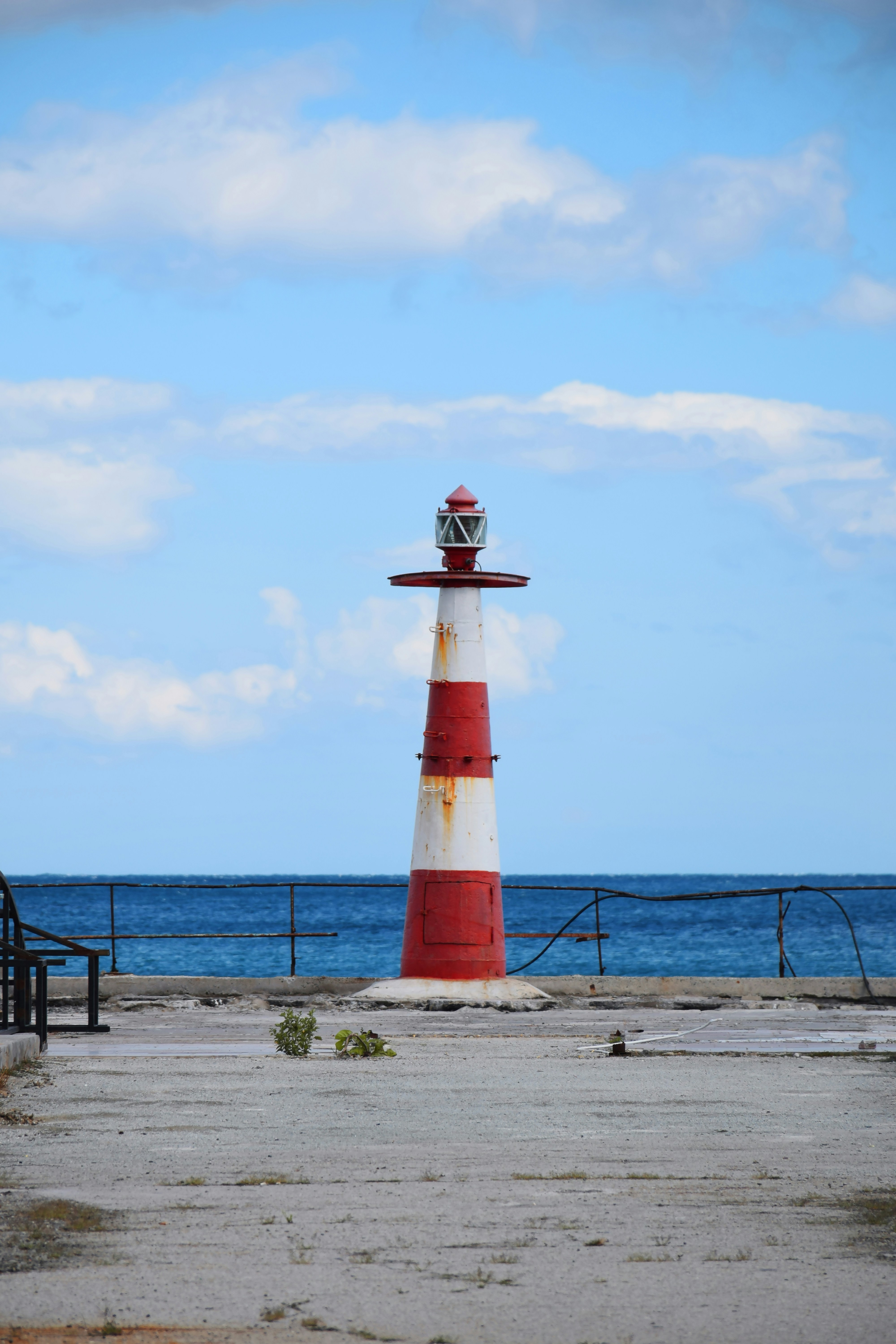 A solitary lighthouse stands on a weathered pier, contrasting against a vibrant blue sky and ocean backdrop.