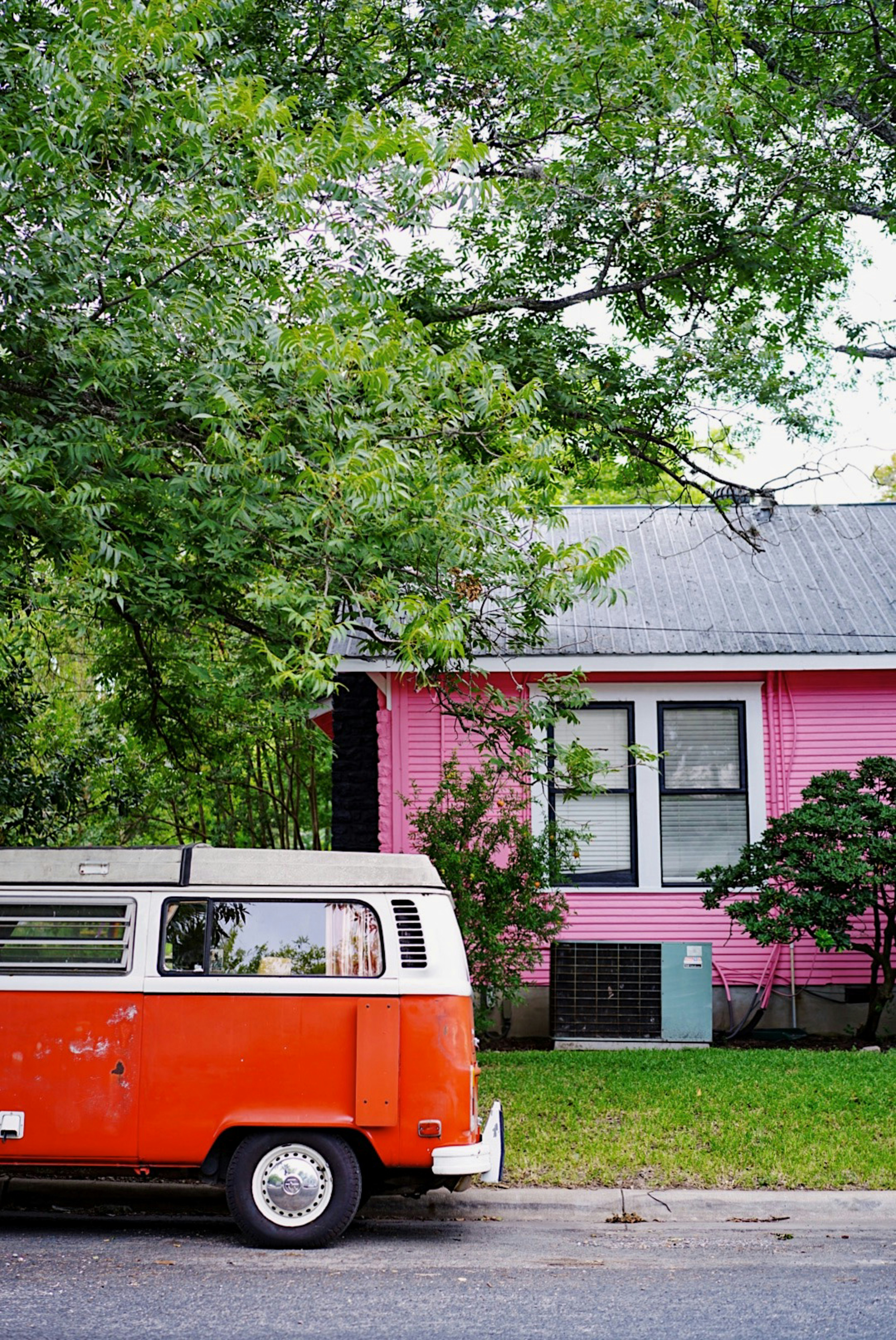 Retro orange VW bus beside a pink cottage framed by green foliage