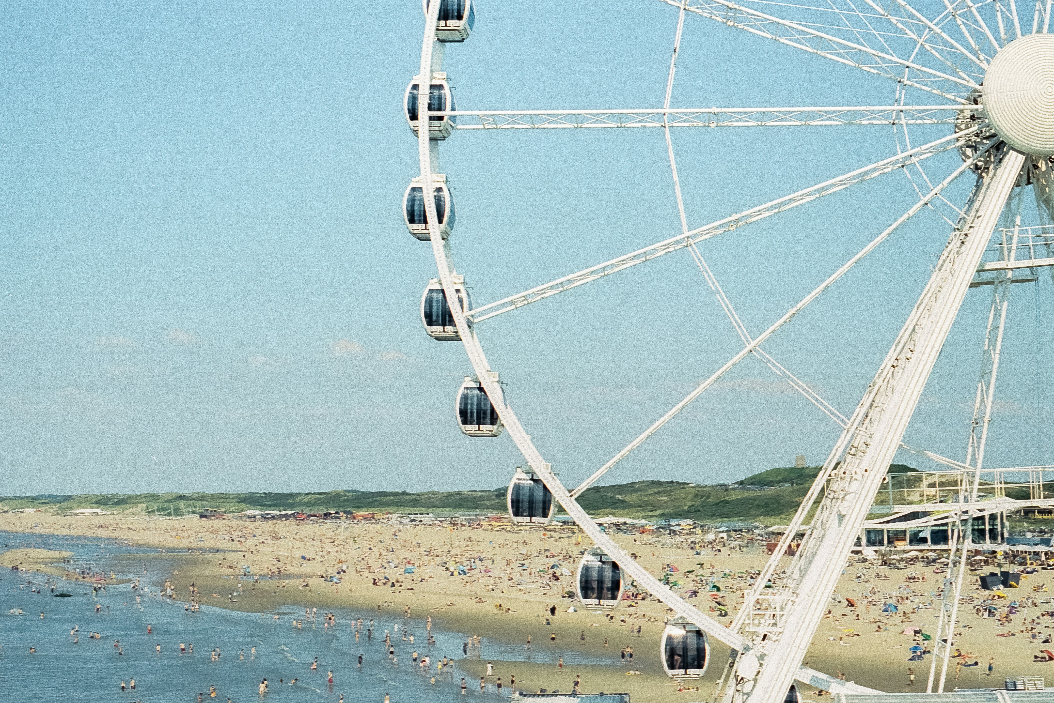 A vibrant beach scene featuring a large Ferris wheel overlooking sunbathers and the shoreline. The atmosphere captures the essence of a lively summer day.
