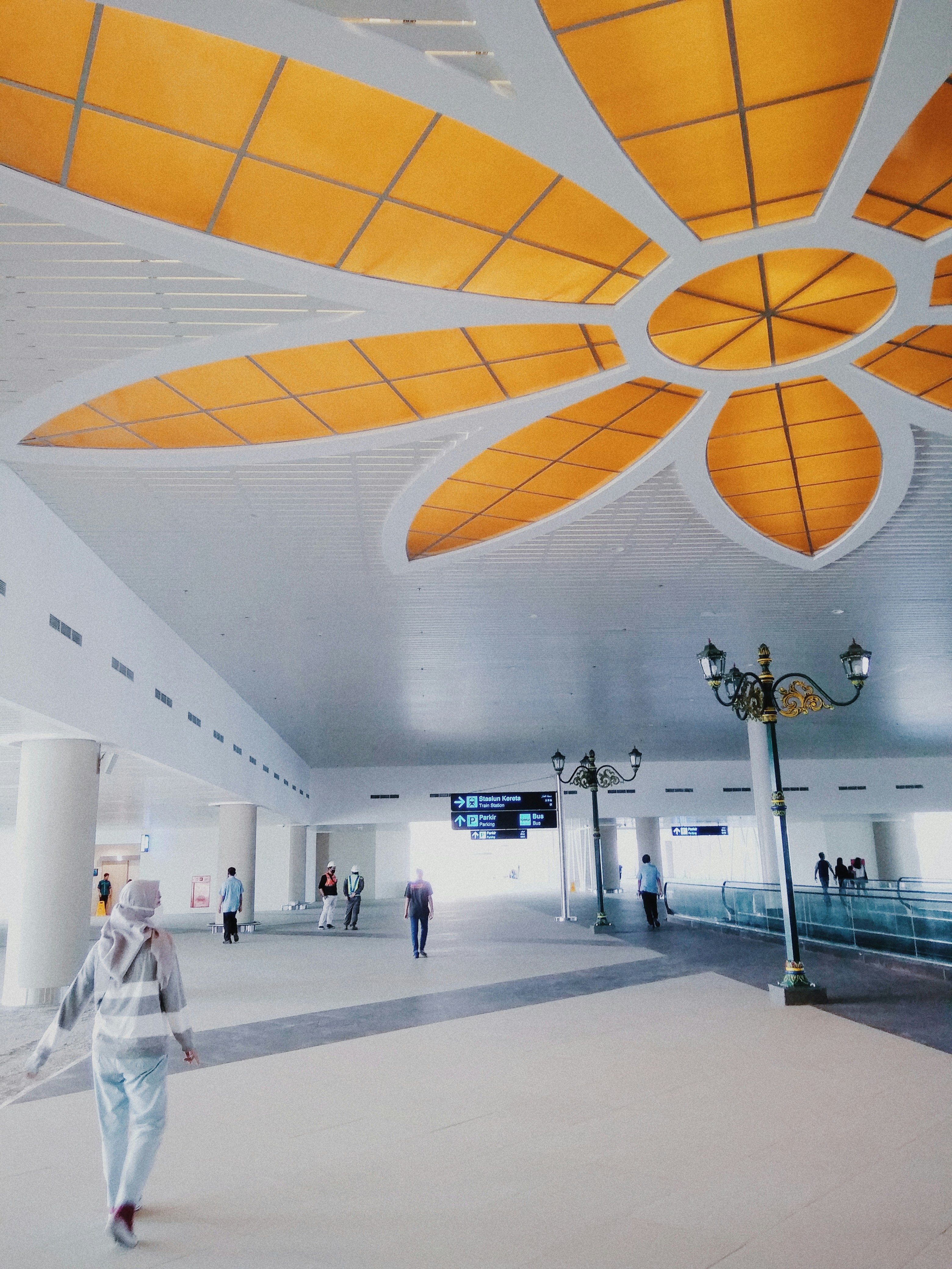 Interior of a contemporary building featuring a striking floral ceiling design and people walking through the spacious area.