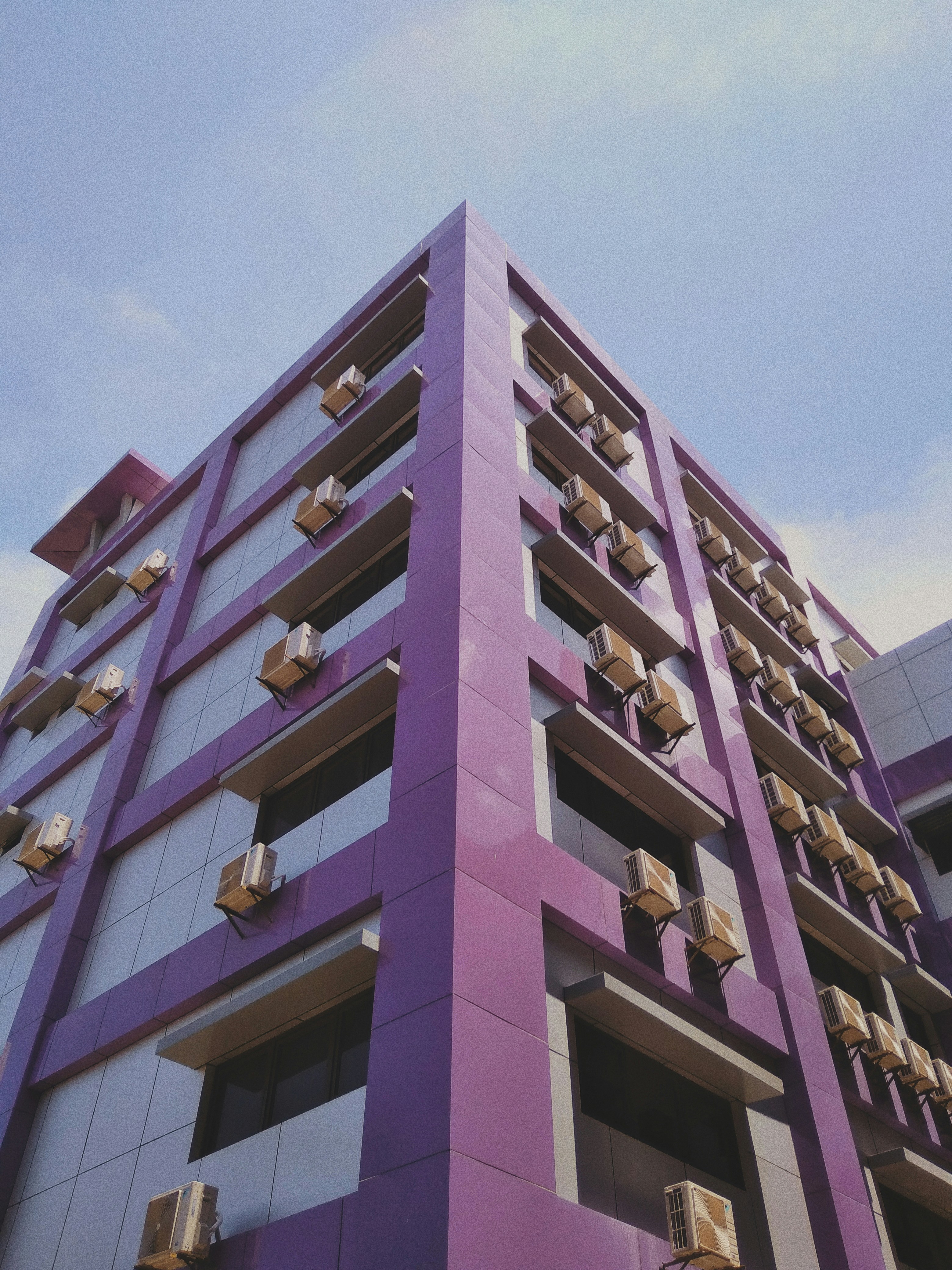 A modern building with a striking purple exterior and multiple air conditioning units, set against a clear blue sky.