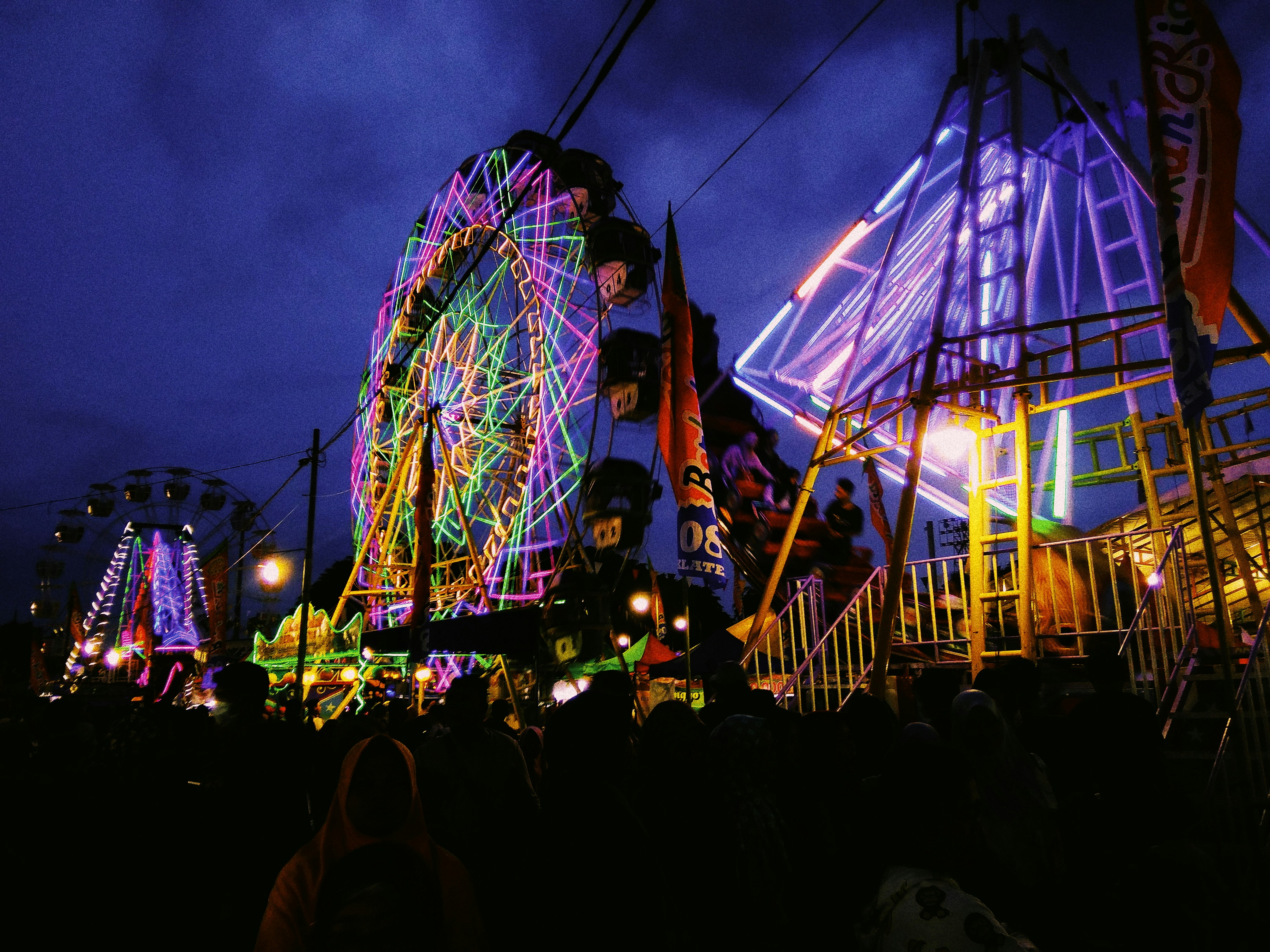 Illuminated Ferris wheels and rides against a twilight sky at a bustling fair.