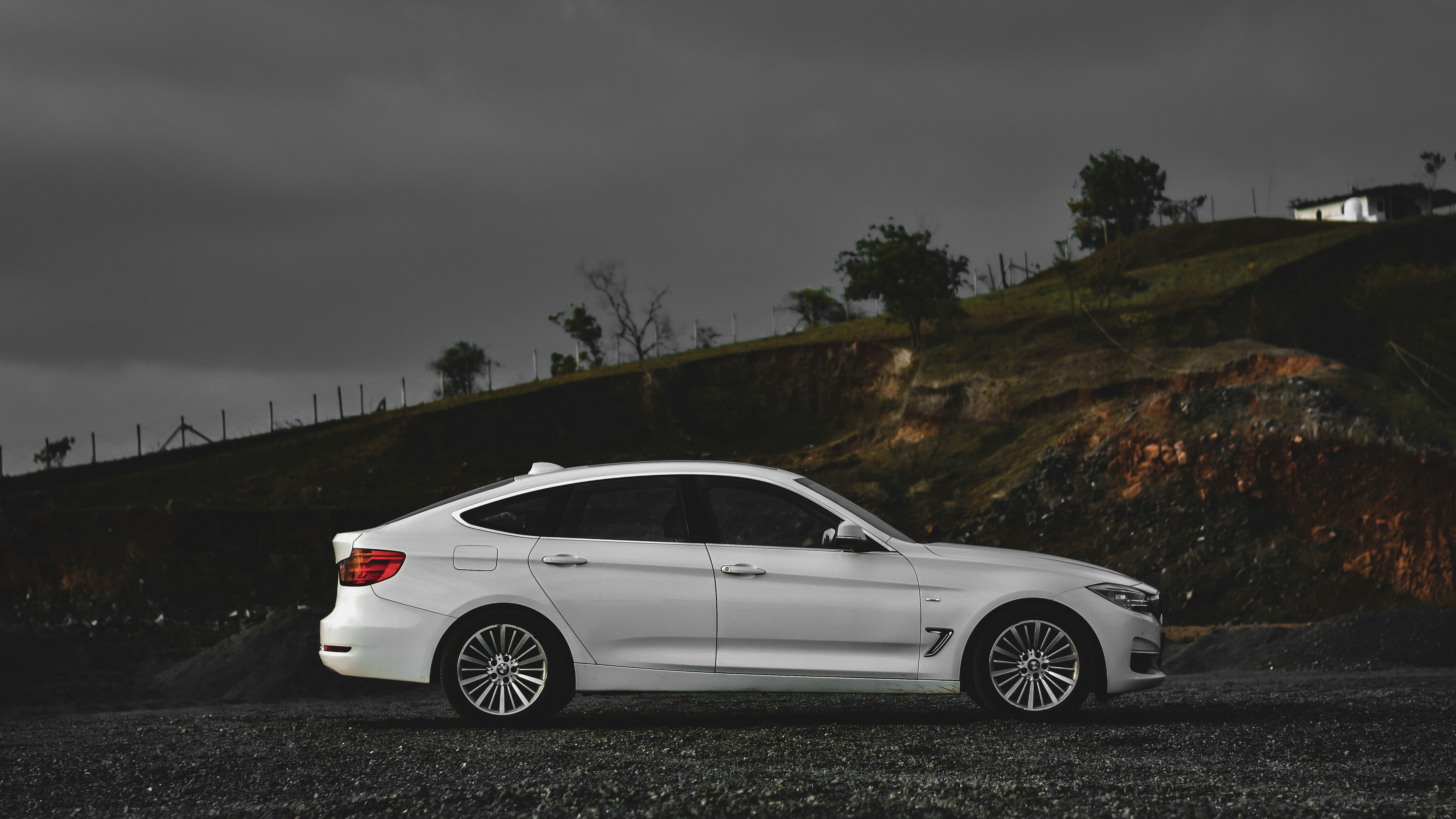 White sedan parked on a dark road with a rugged hillside in the background.
