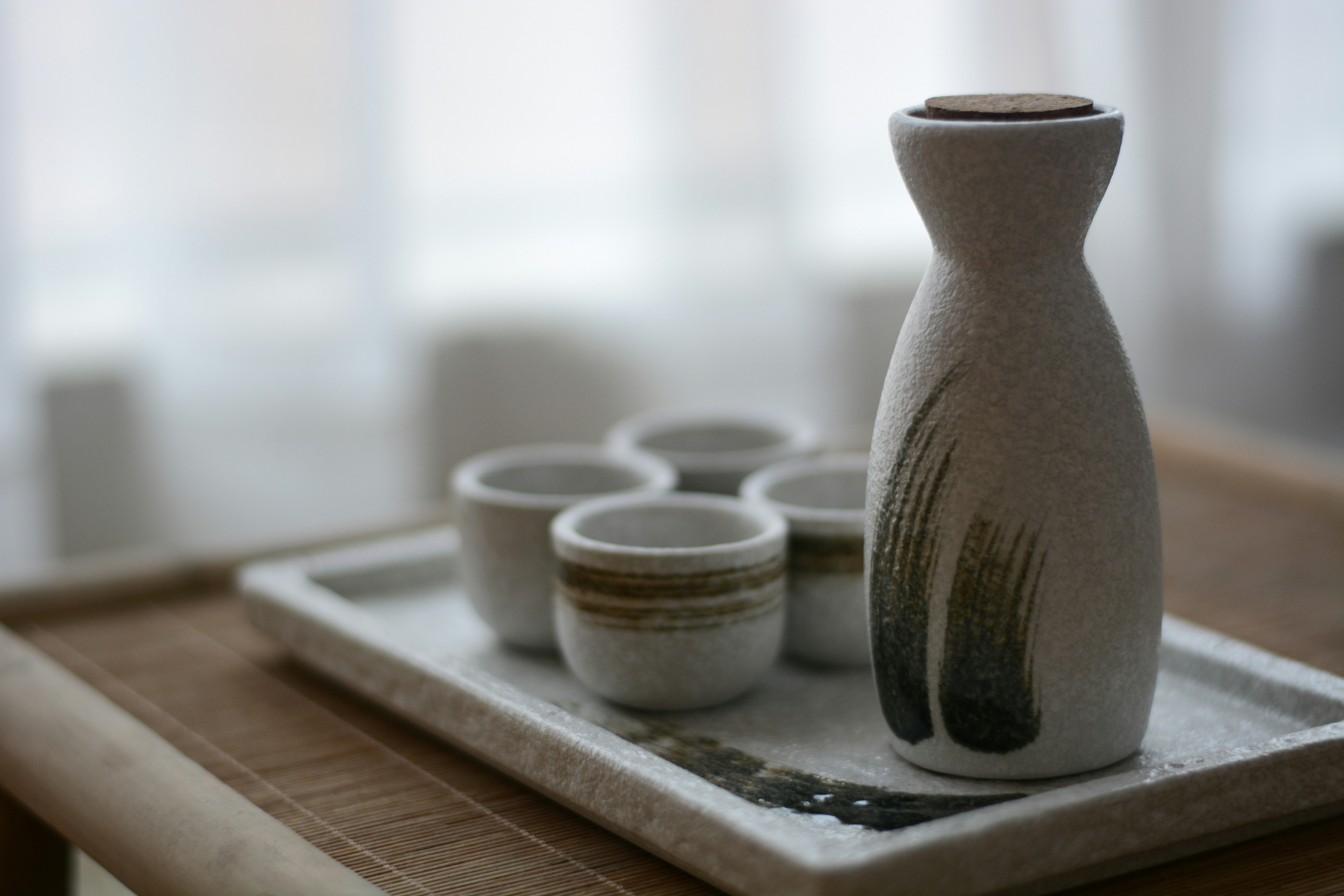 Elegant ceramic sake set arranged on a textured tray, featuring a slender bottle and small cups, bathed in soft natural light.