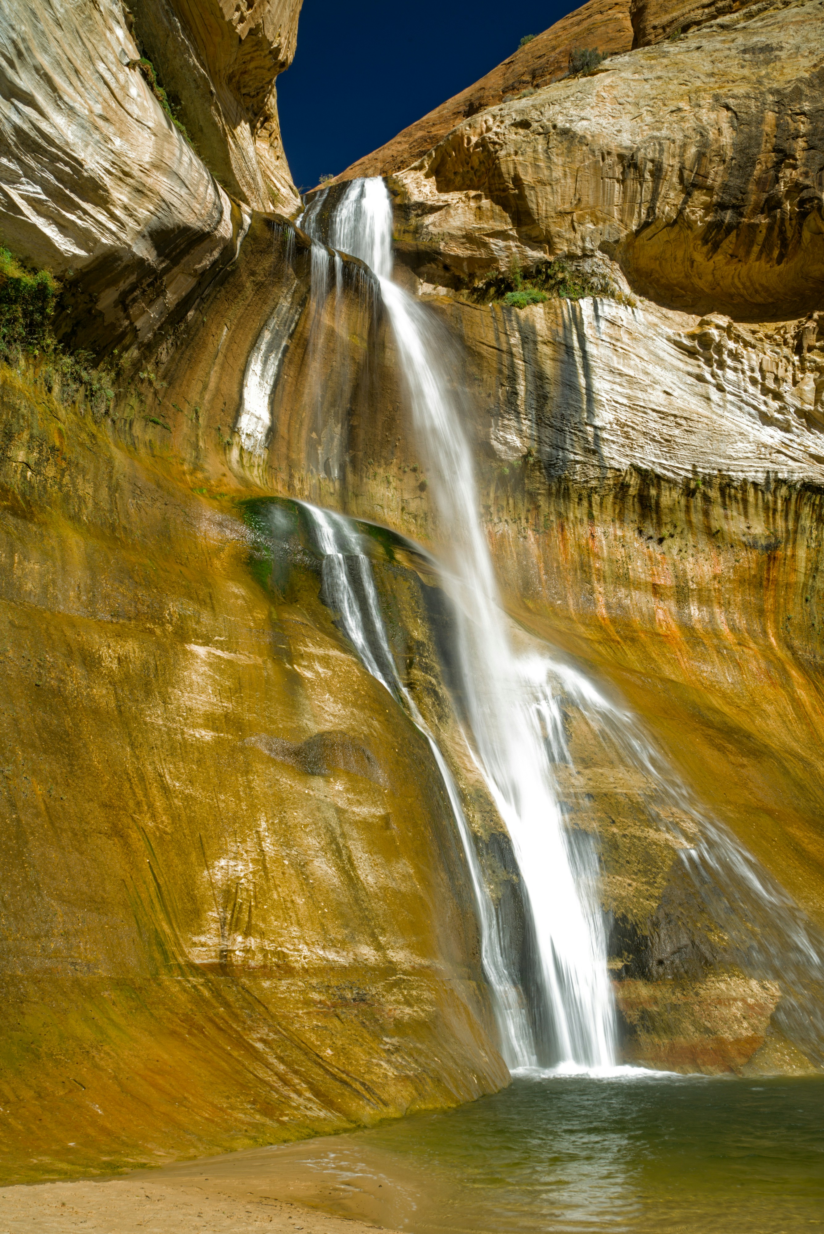 Waterfall cascading over vibrant rock formations into a serene pool below.