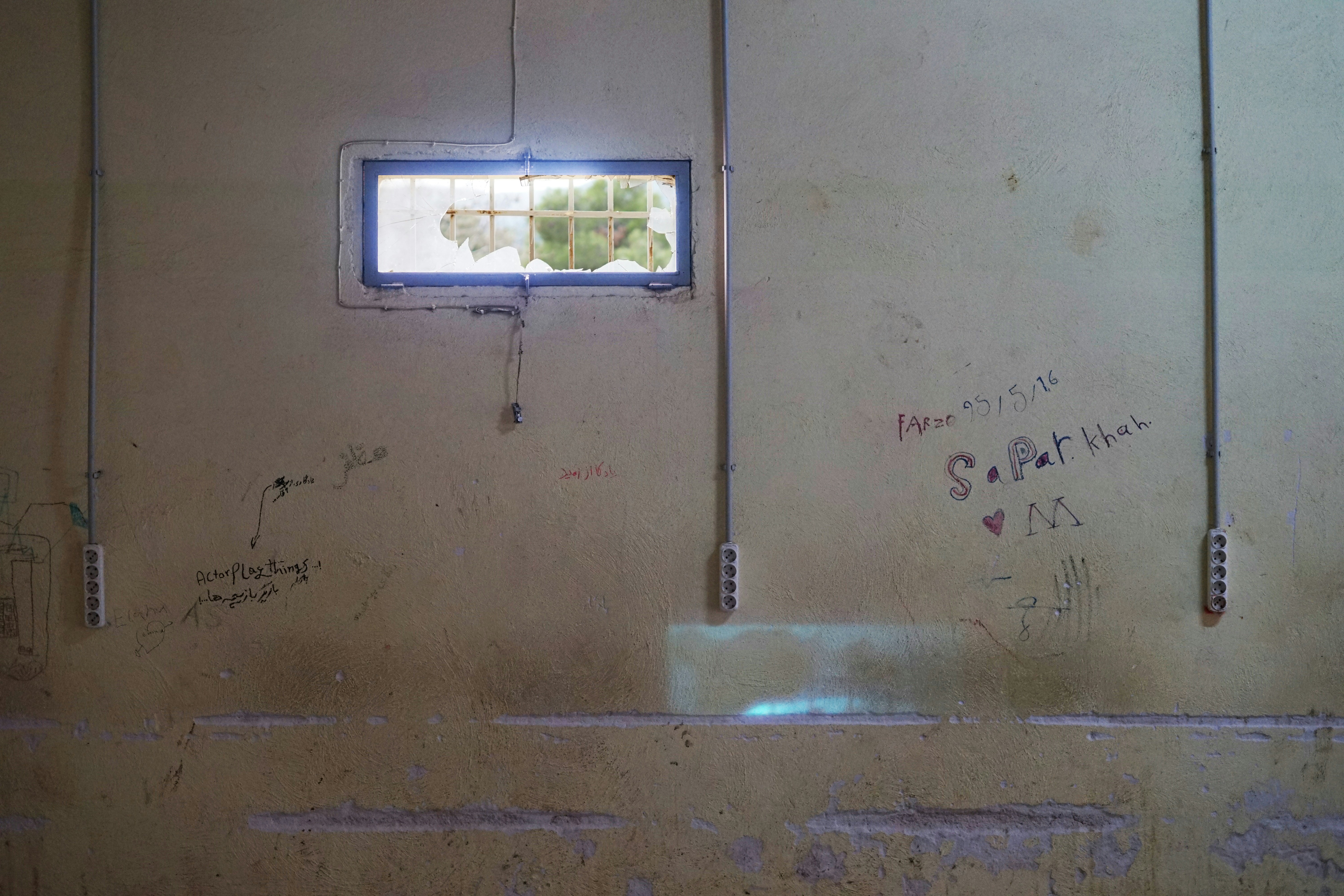 Sunlight streaming through a small window illuminates a weathered wall adorned with faint graffiti and peeling paint.