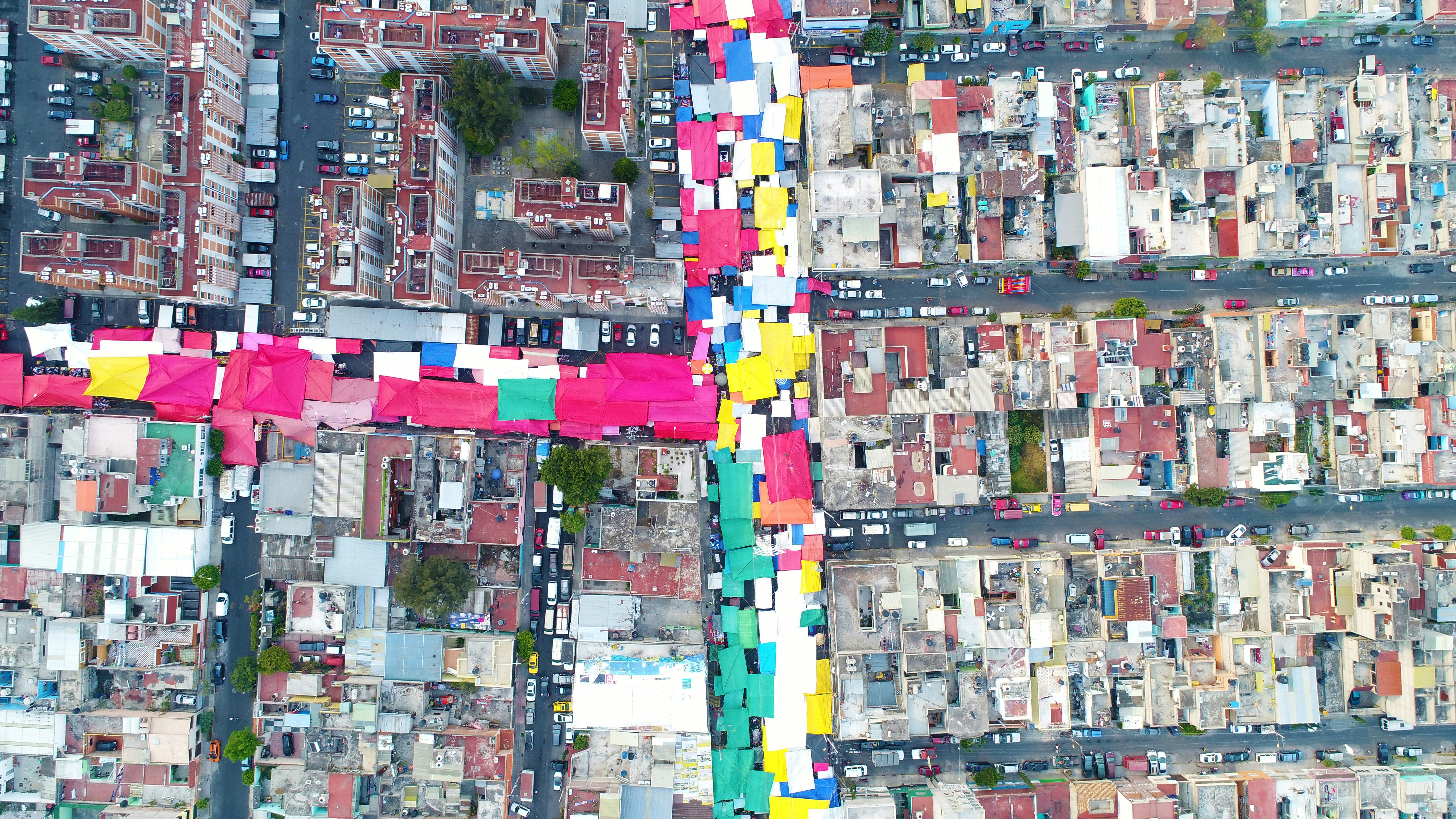 Aerial view of colorful market tents lining the streets between residential buildings.