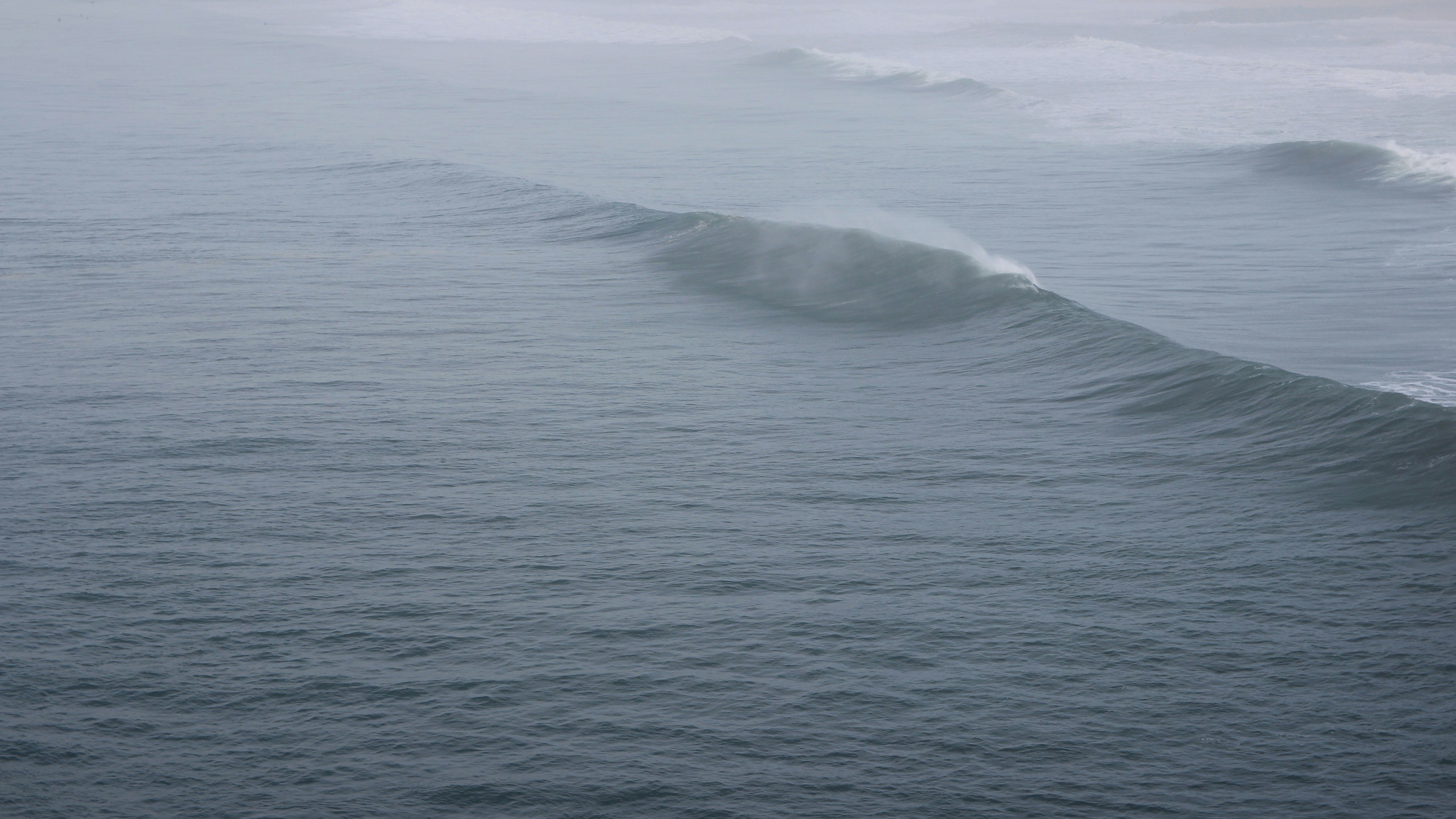 Gentle waves undulating across a misty seascape, creating a serene atmosphere. The subtle interplay of light and water enhances the tranquil mood.