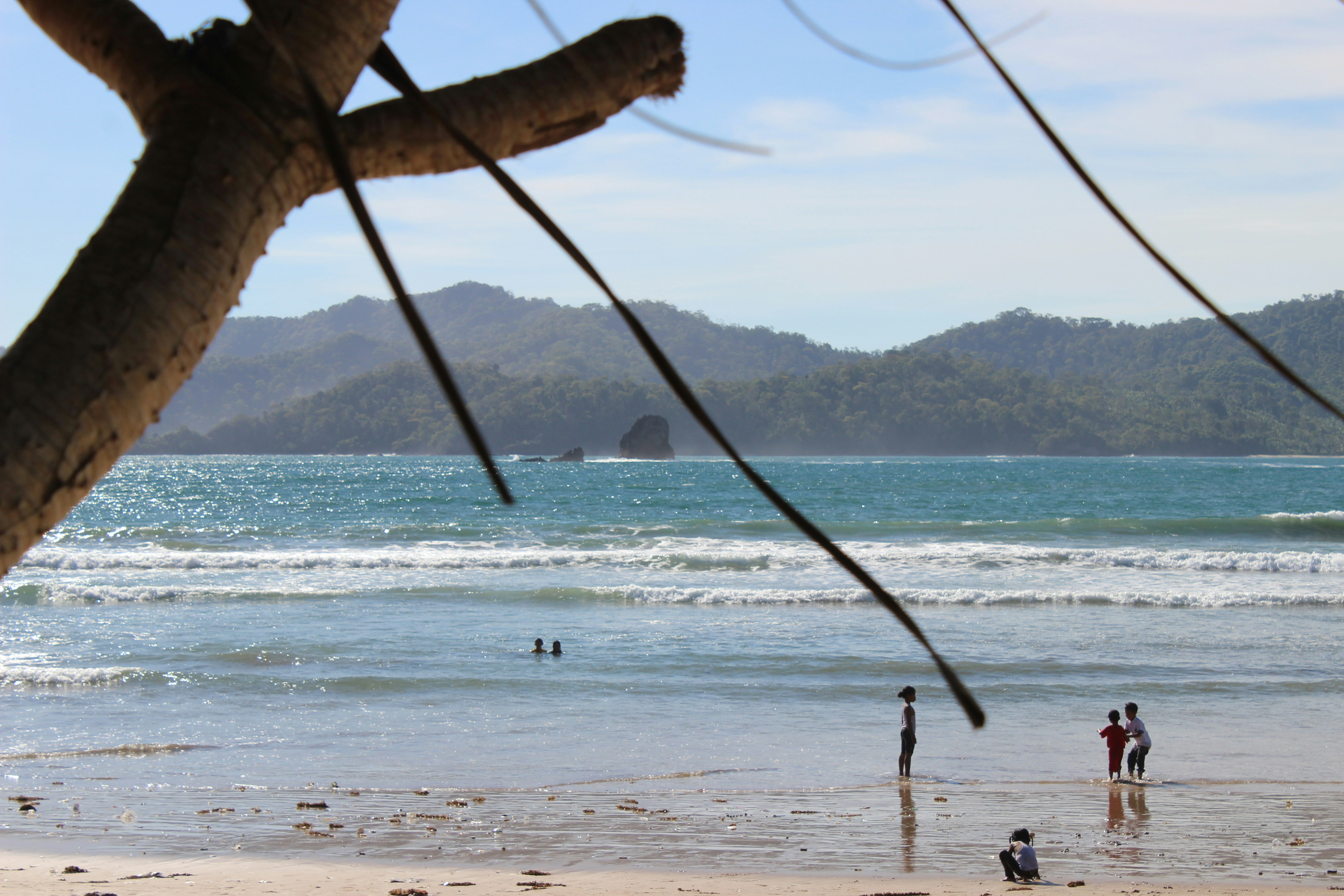 People enjoying a sunny day on a sandy beach with distant mountains under a clear blue sky.