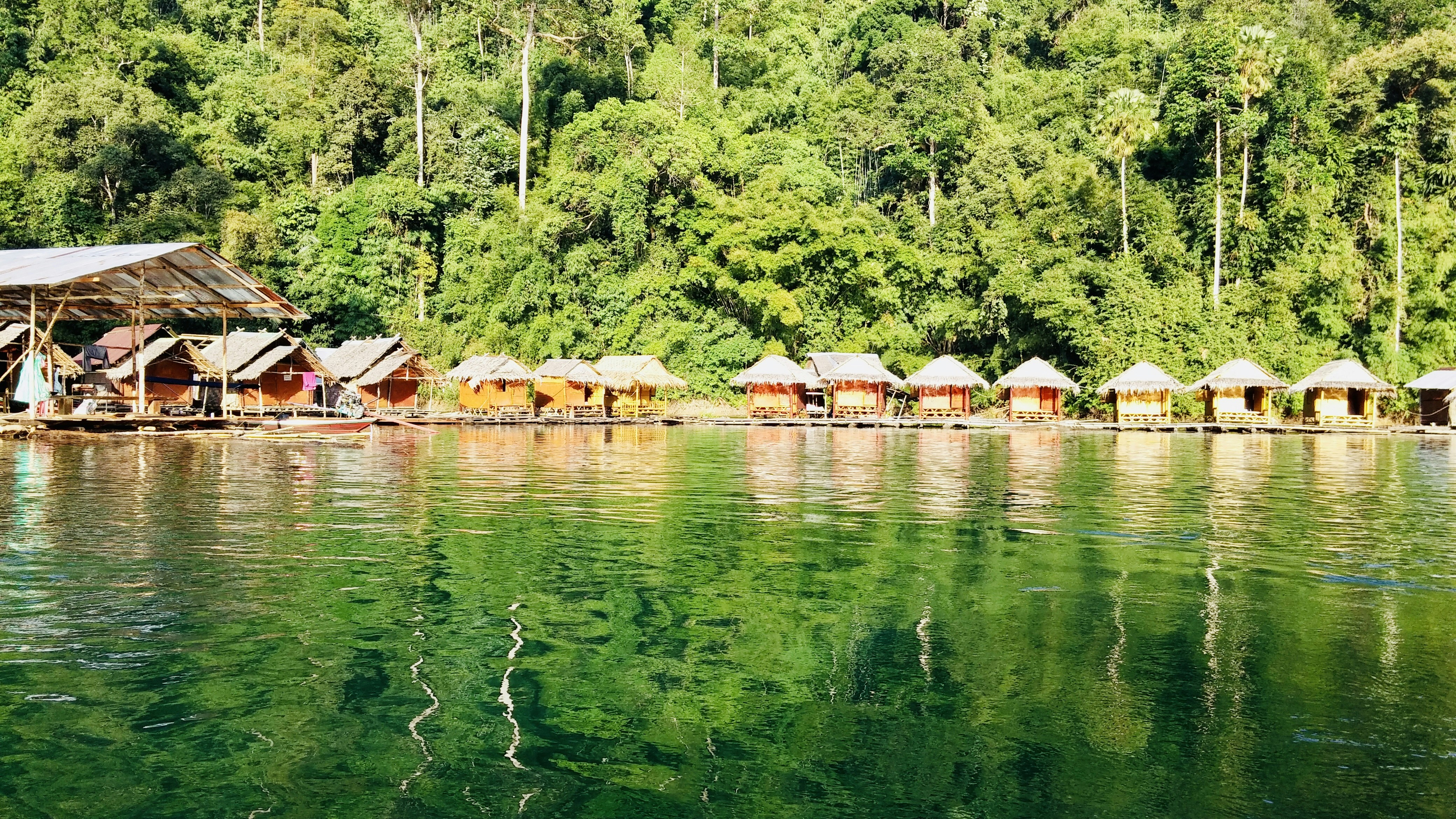 Row of rustic huts nestled by a lush green jungle and tranquil river.