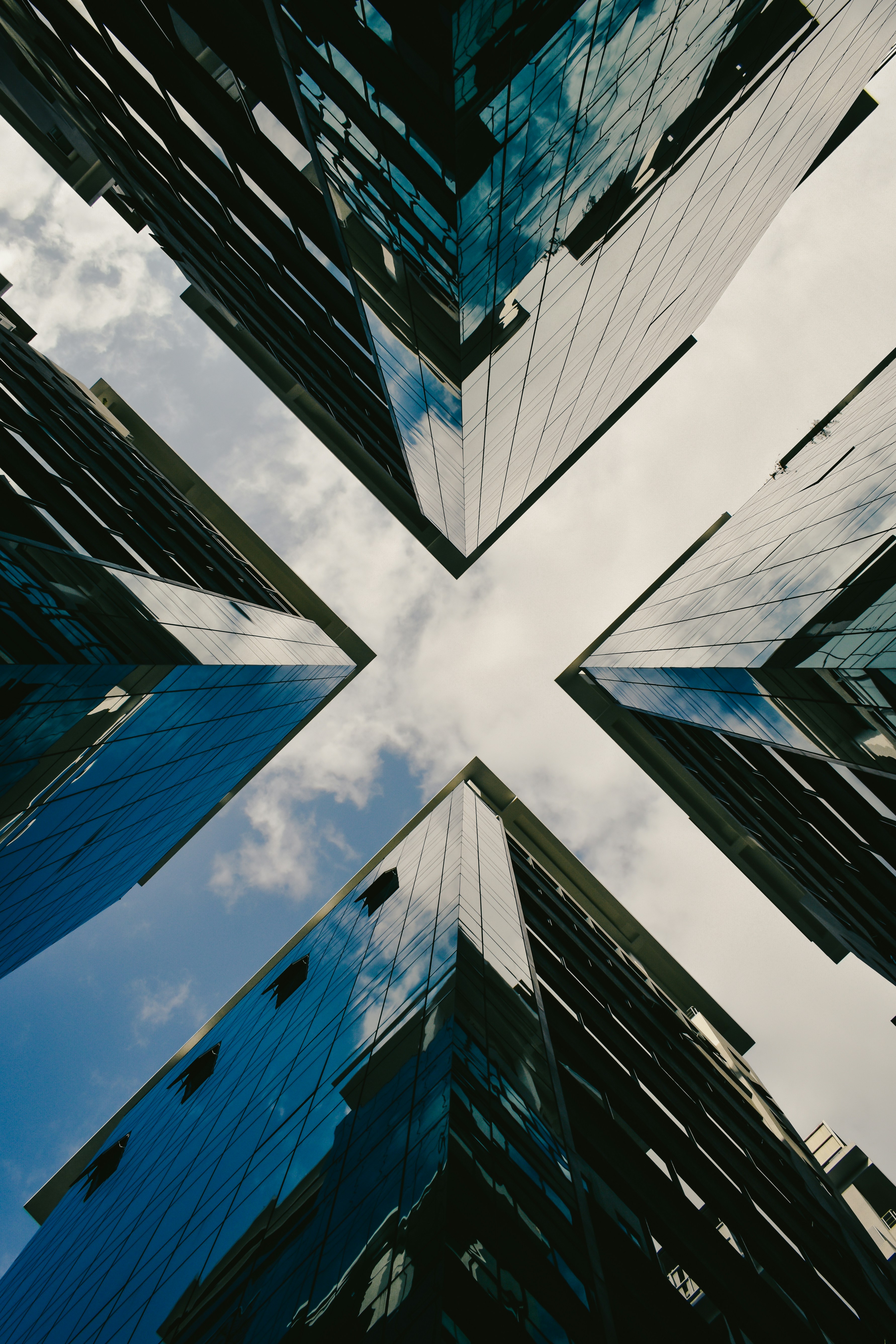 Symmetrical view of modern skyscrapers reflecting clouds, creating a striking geometric pattern.