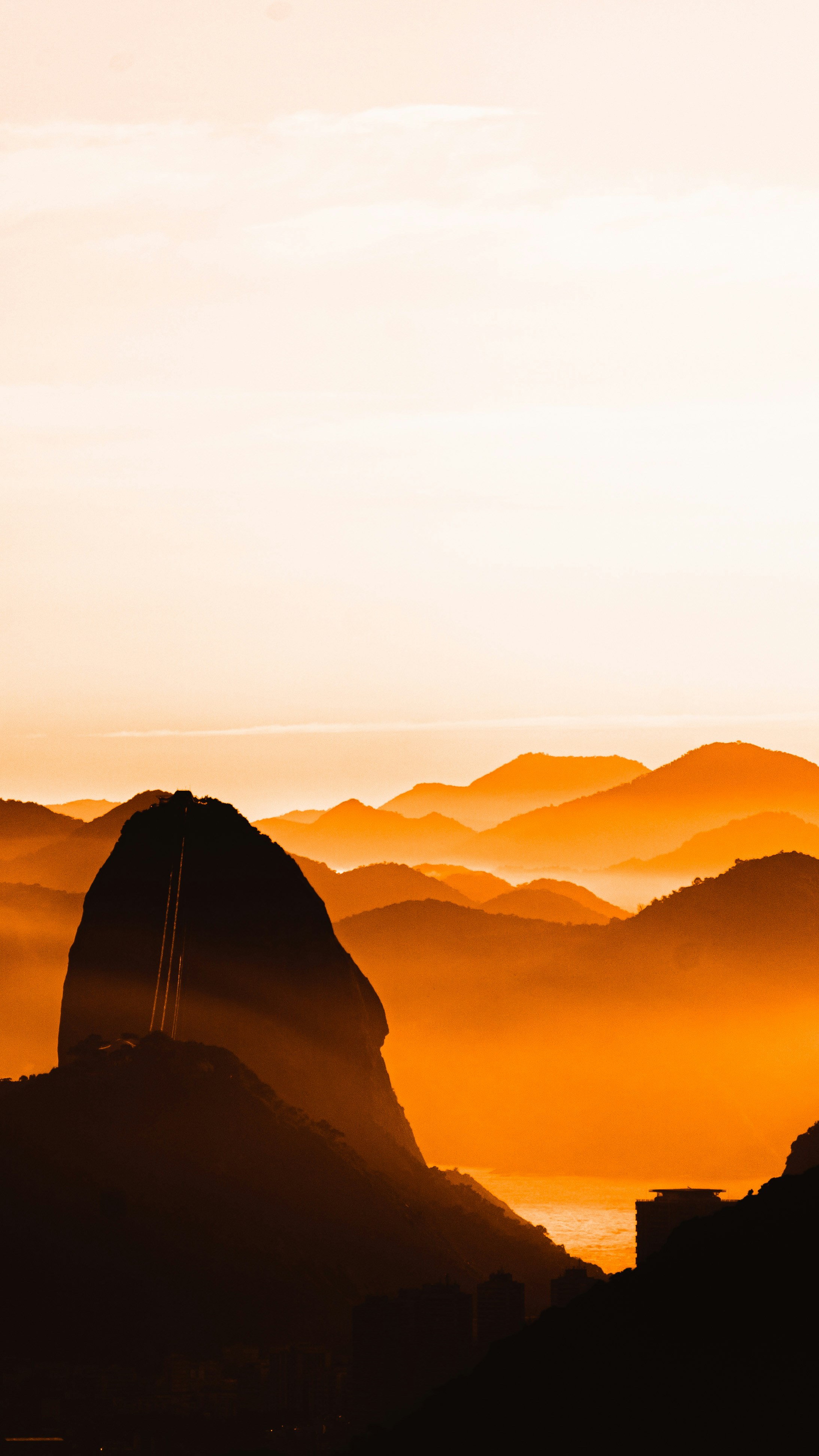 Silhouette of Sugarloaf Mountain against a backdrop of layered hills bathed in warm orange hues at sunset.