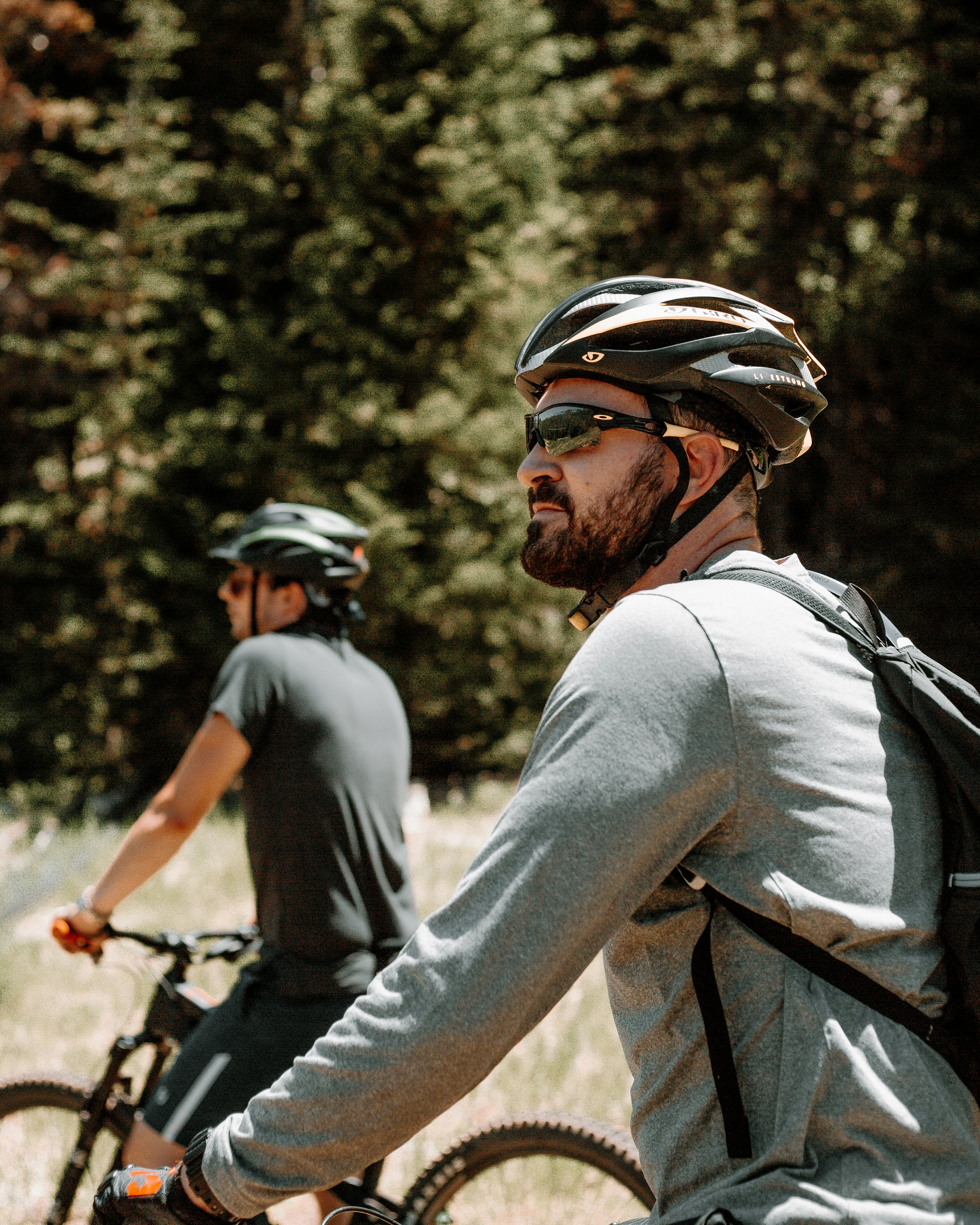 Two cyclists pause amidst a lush forest backdrop, showcasing the thrill of mountain biking in nature's embrace.