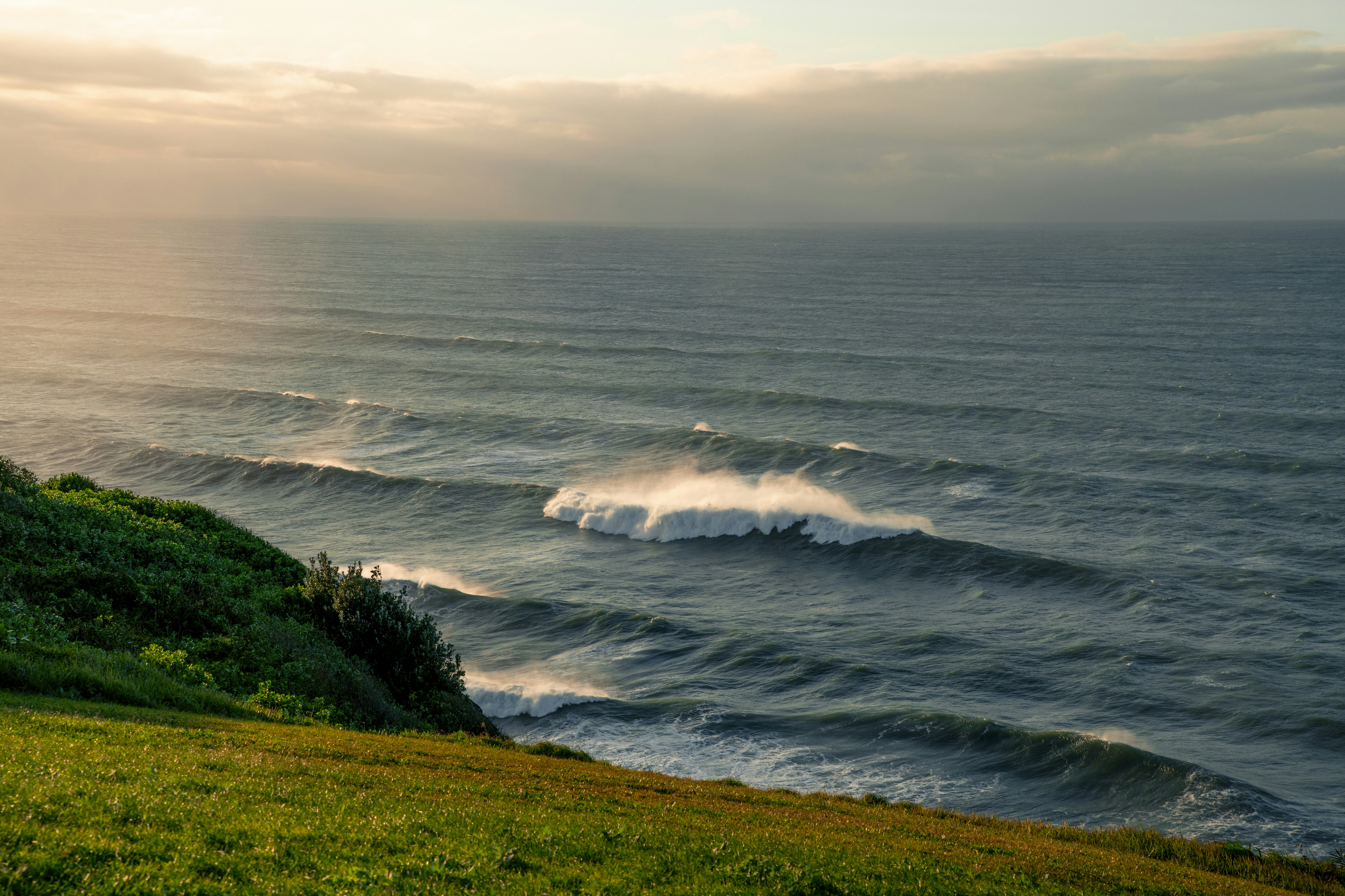 Waves crashing against the rocky shoreline under a cloudy sky at sunset.