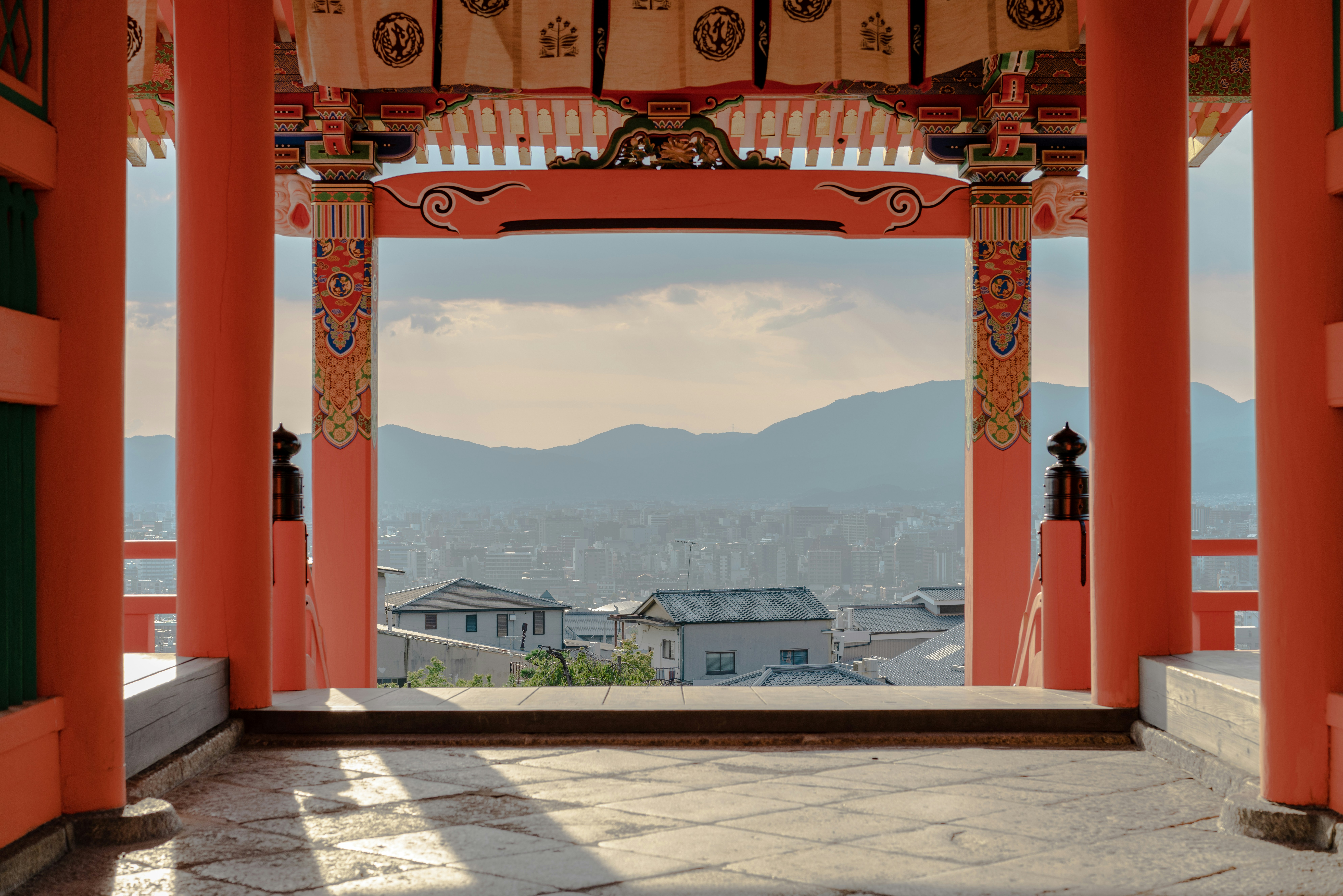 Vibrant red pillars frame a panoramic view of a distant mountain range and cityscape, showcasing traditional architecture against a serene backdrop.
