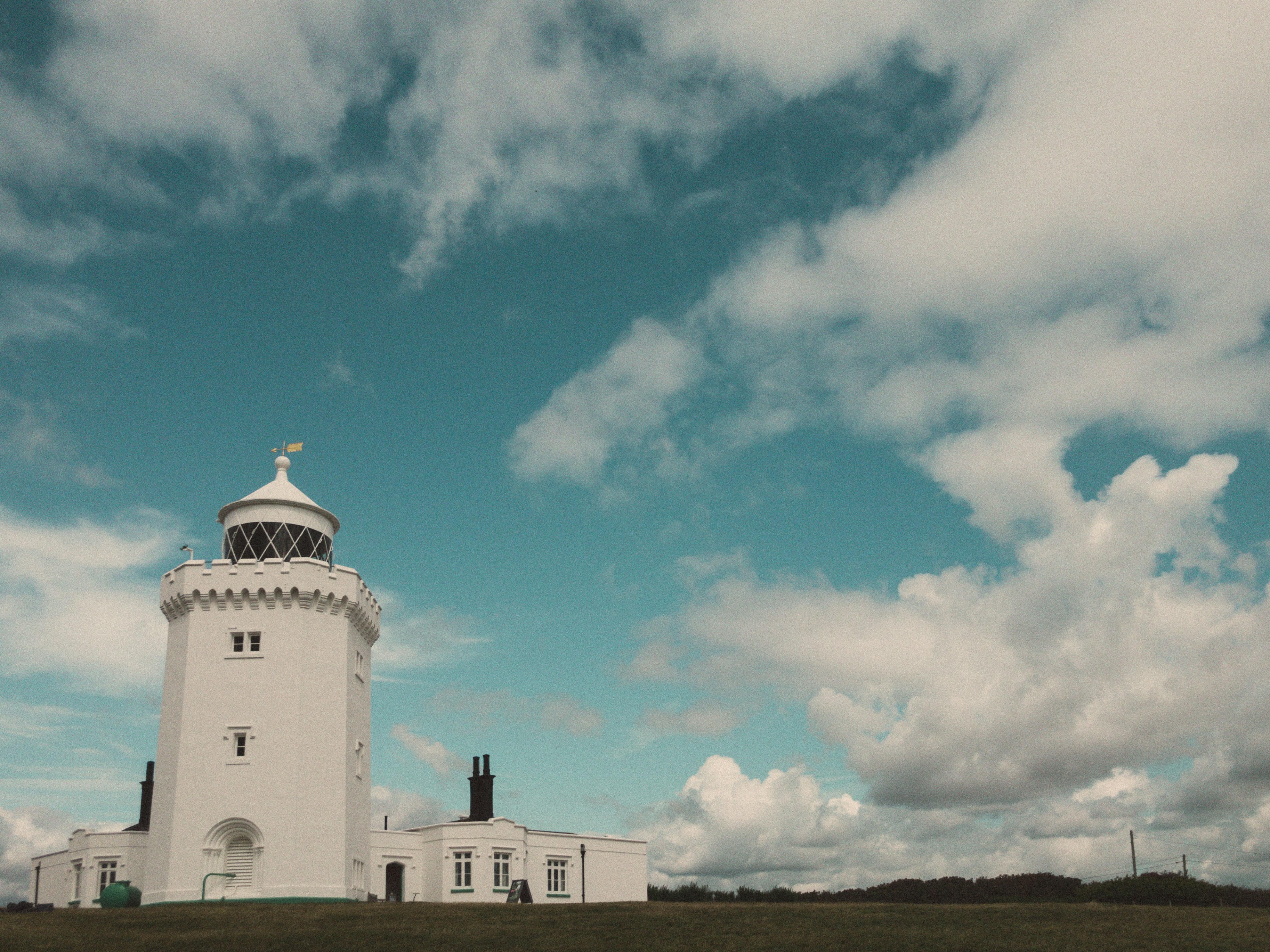 White lighthouse and building beneath expansive sky filled with scattered clouds.