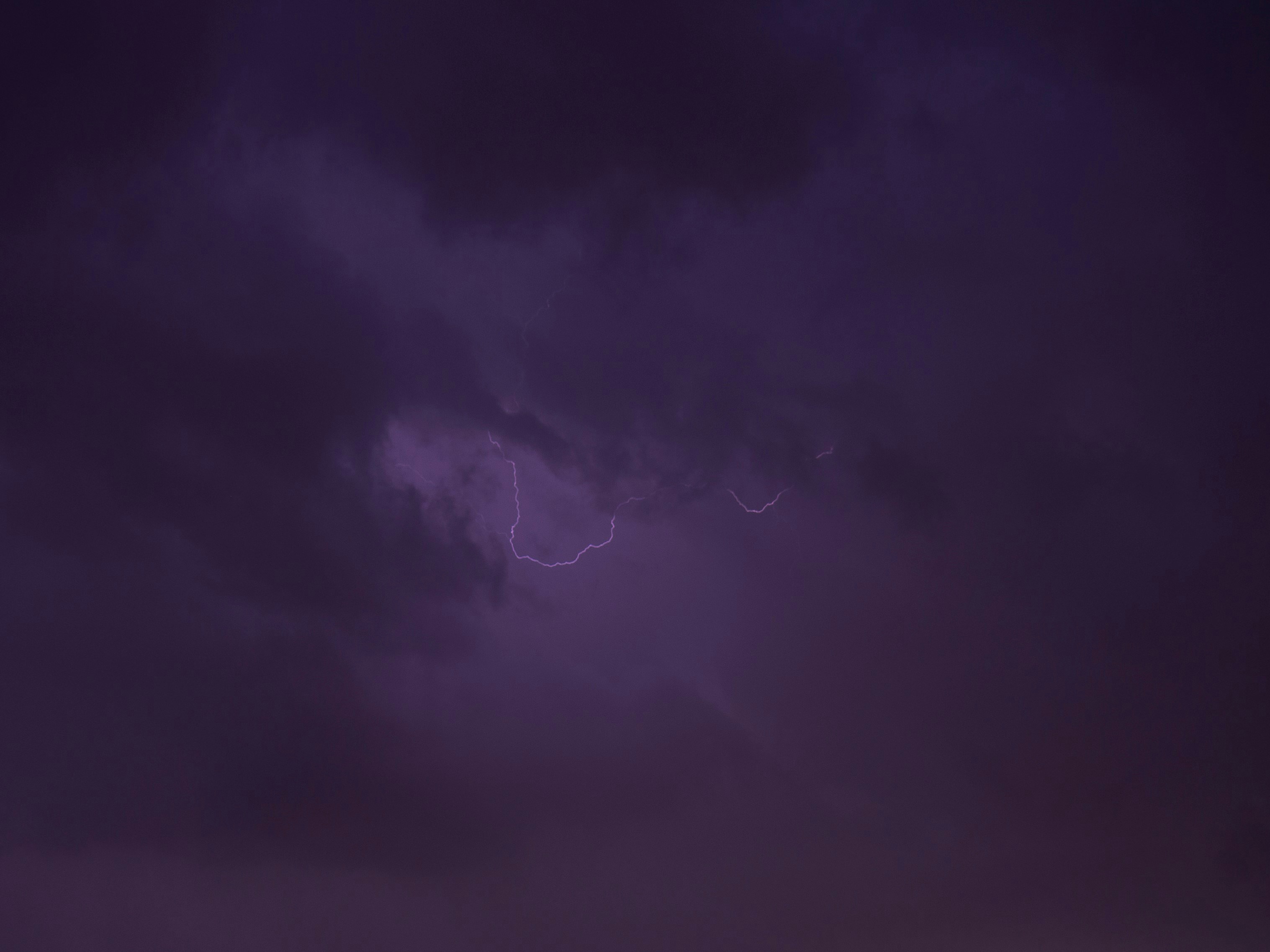 Fleeting lightning bolts illuminate dark, swirling clouds in a dramatic evening sky.