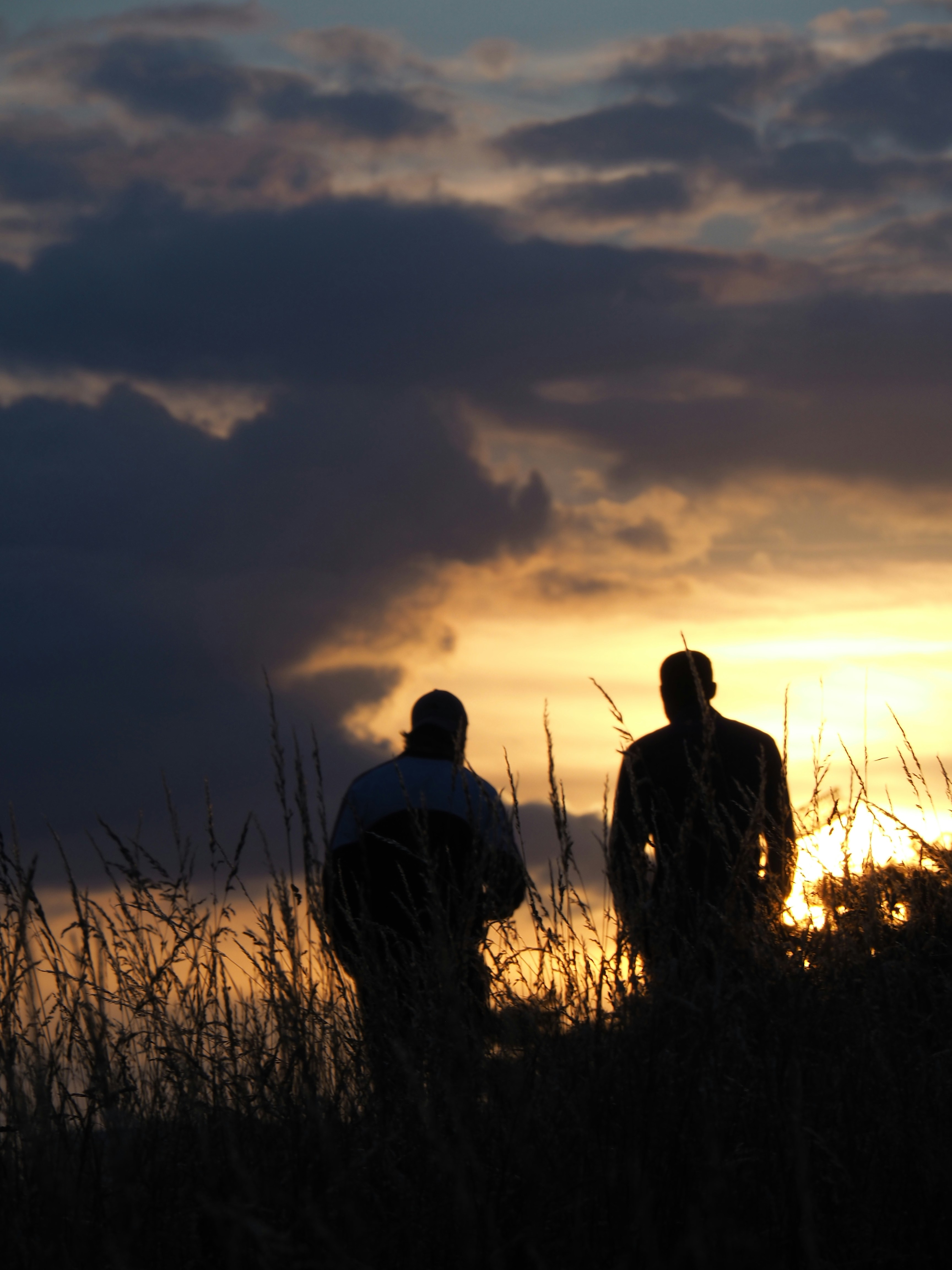 Silhouettes of two men standing in a grassy field against a dramatic sunset sky.