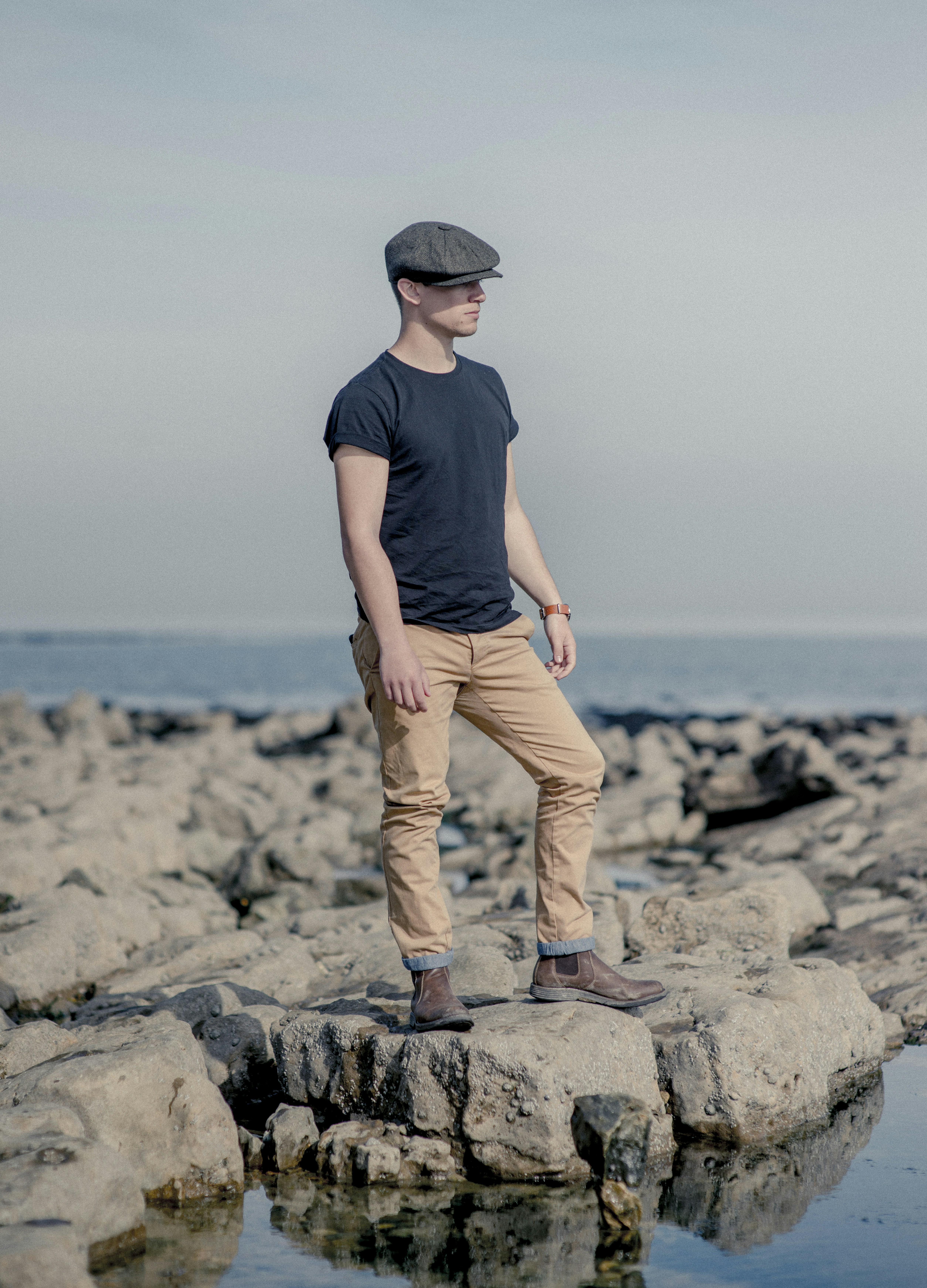 Person standing on rugged rocks by the sea under a clear sky.