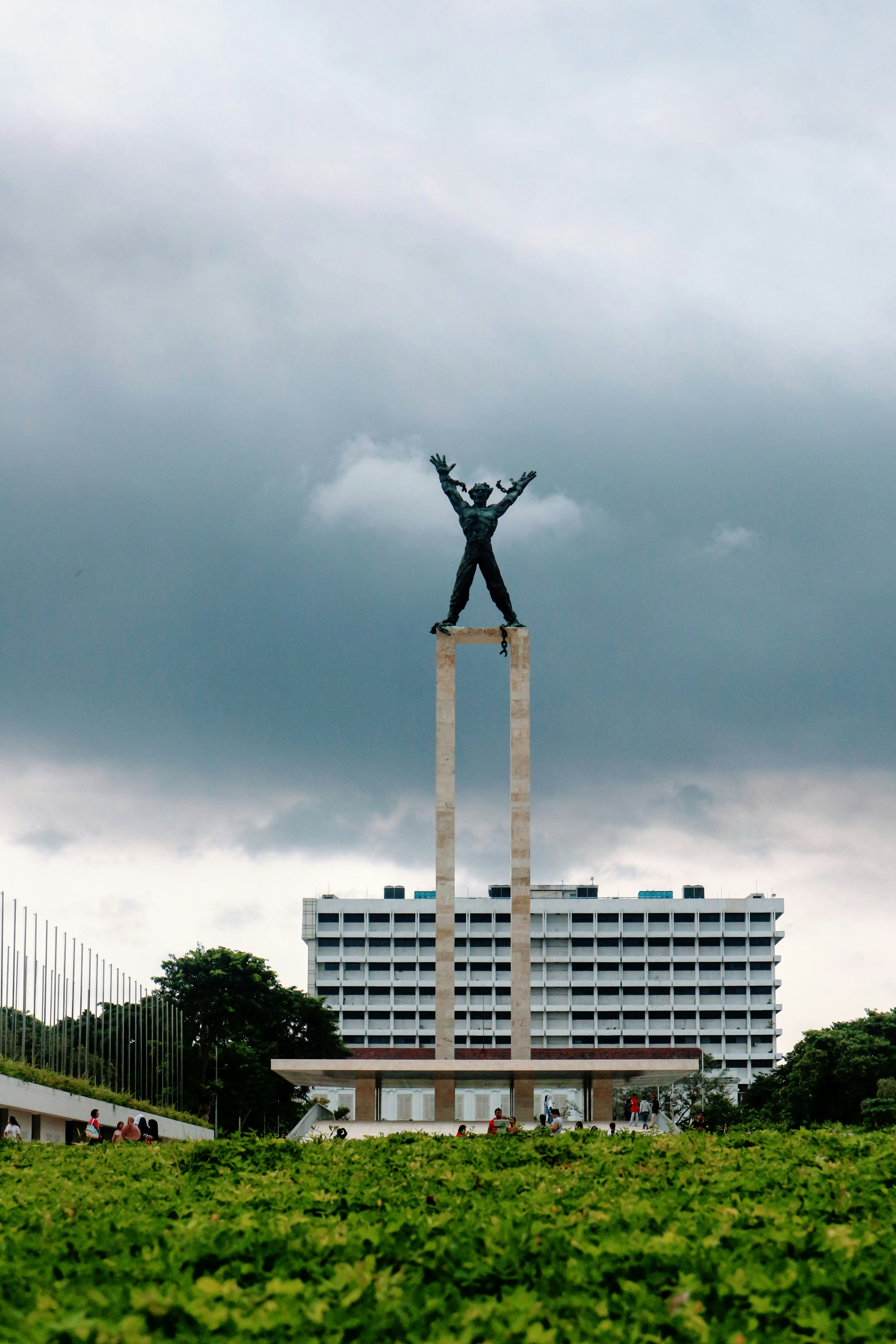 A towering statue of a figure with outstretched arms stands atop a pedestal, symbolizing hope and strength against a backdrop of dramatic clouds.