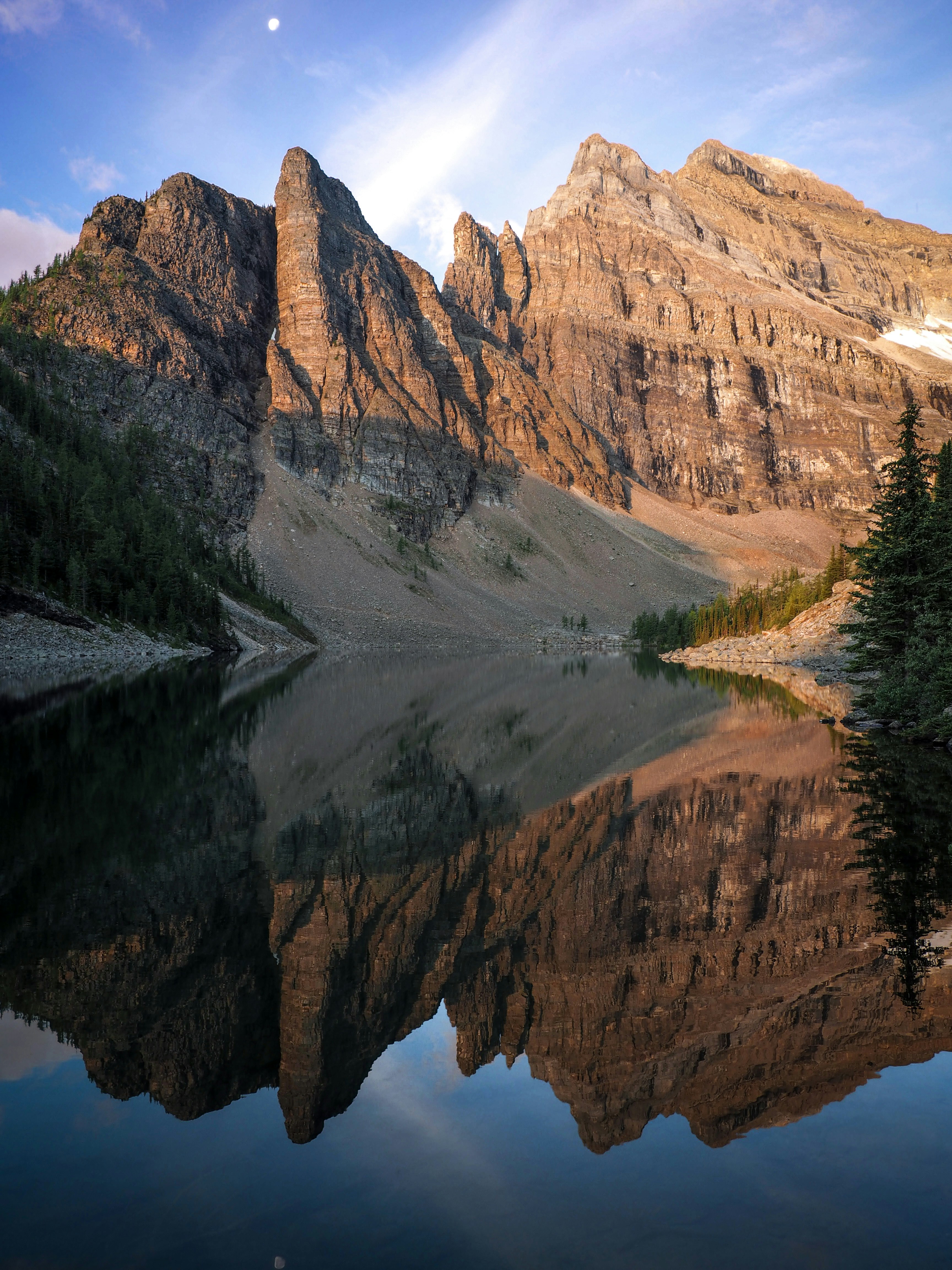 Towering rocky cliffs reflected in a serene lake, surrounded by lush greenery and a clear sky.