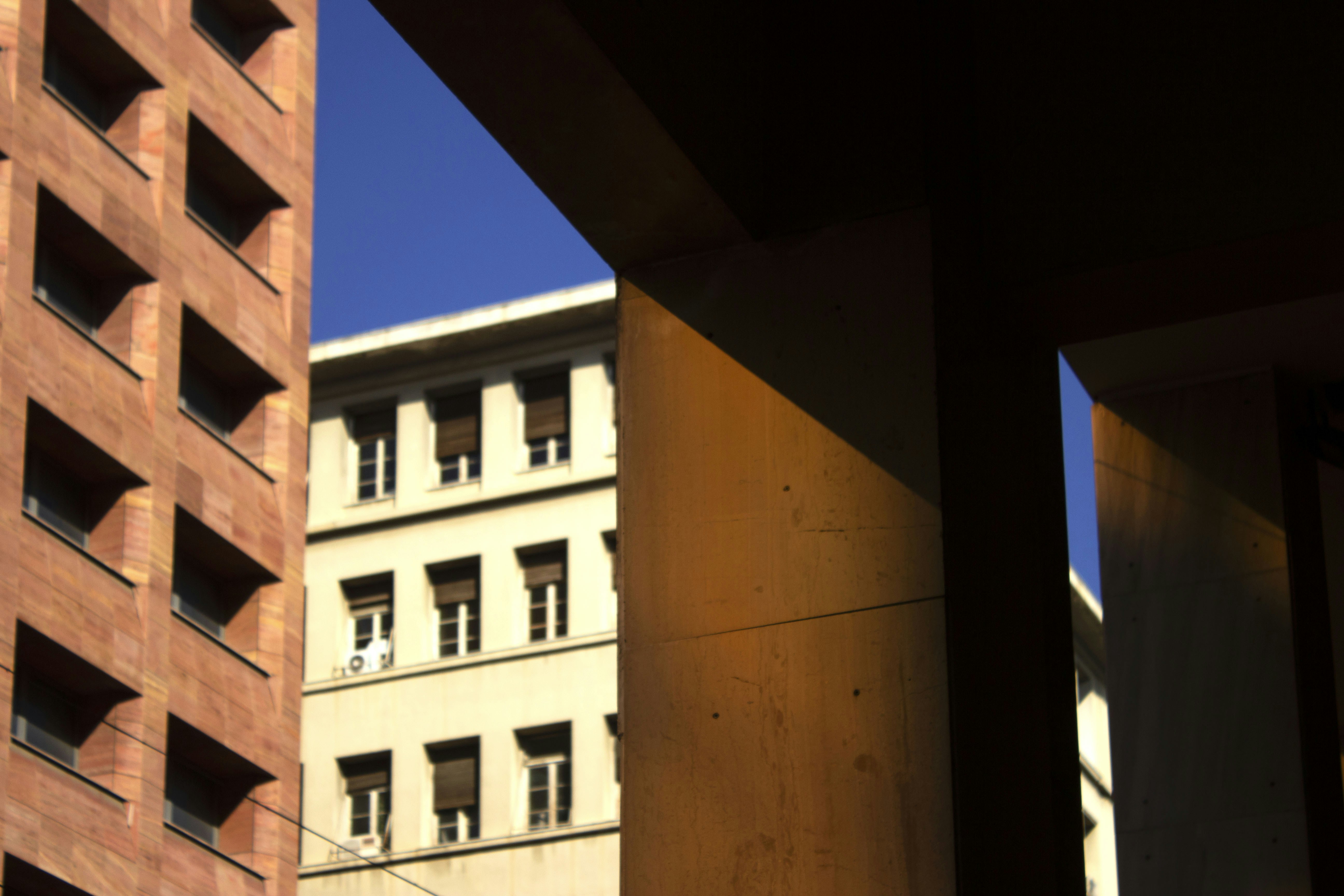 Abstract view of urban architecture framed by contrasting building facades and a clear blue sky. The interplay of light highlights structural details.