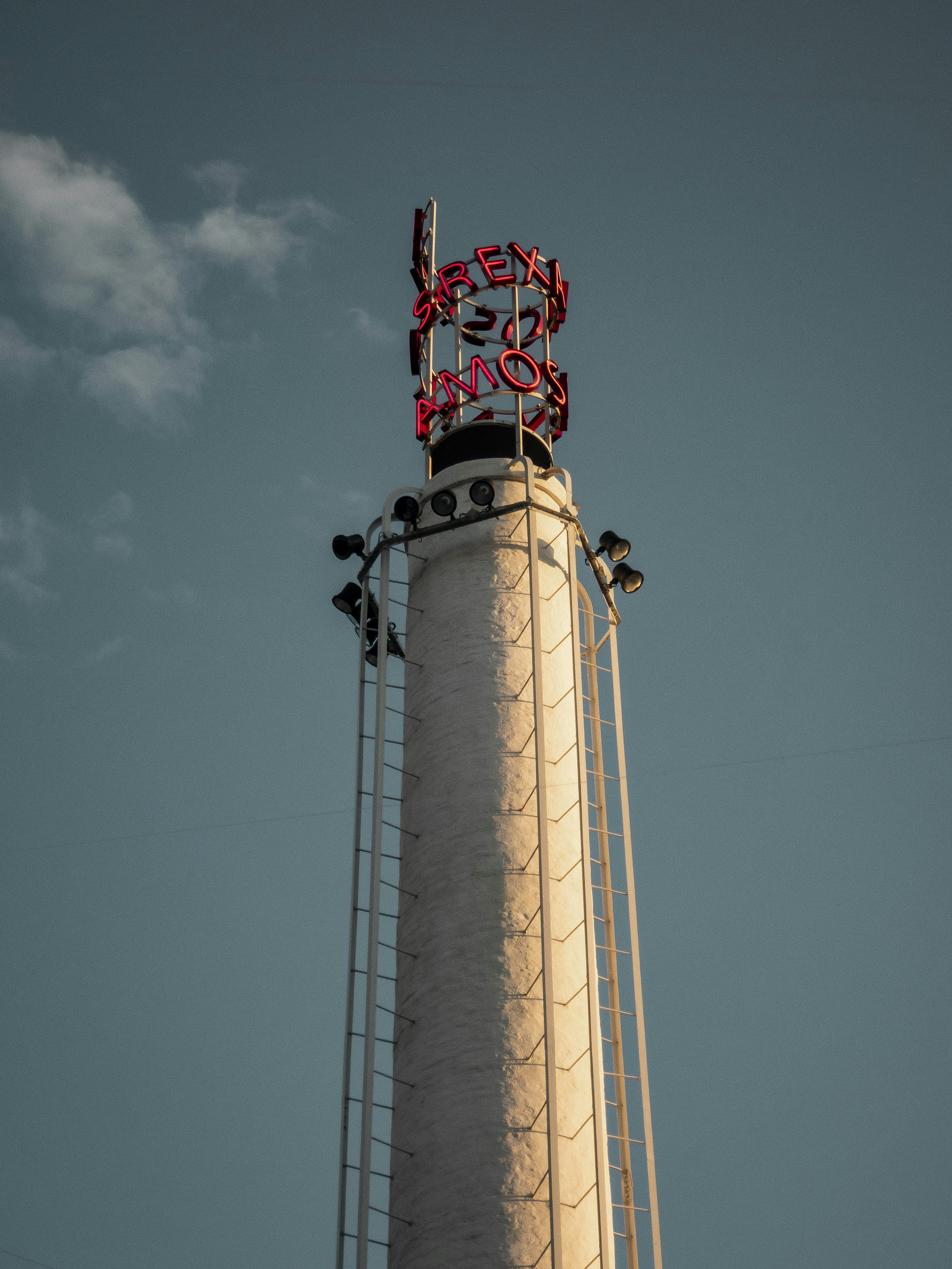 A tall, illuminated sign atop a column, showcasing retro neon letters against a clear sky. The structure hints at a bygone era of vibrant signage.