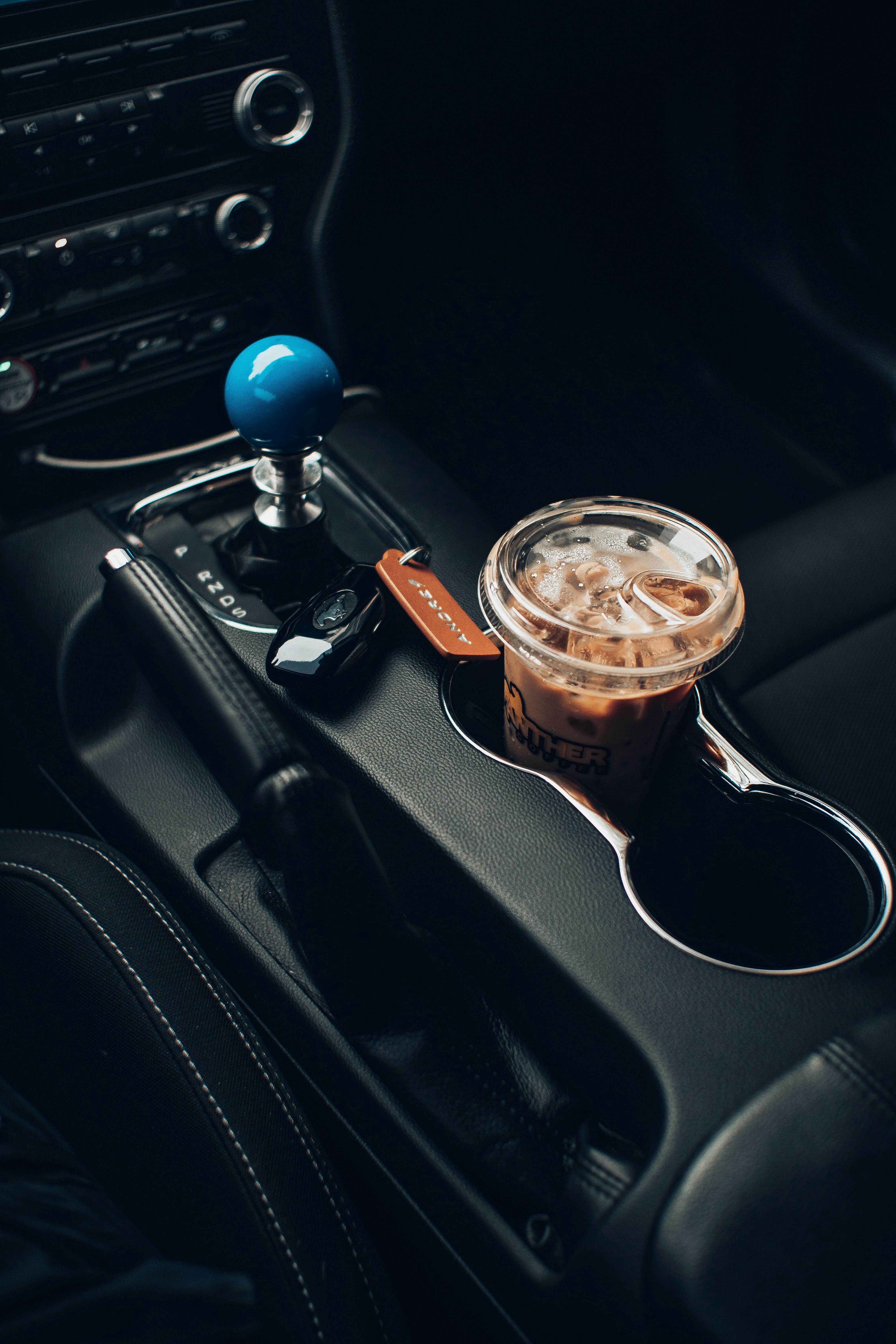 Iced coffee resting in a car's cup holder beside a vibrant gear shift. The sleek interior design highlights modern automotive aesthetics.