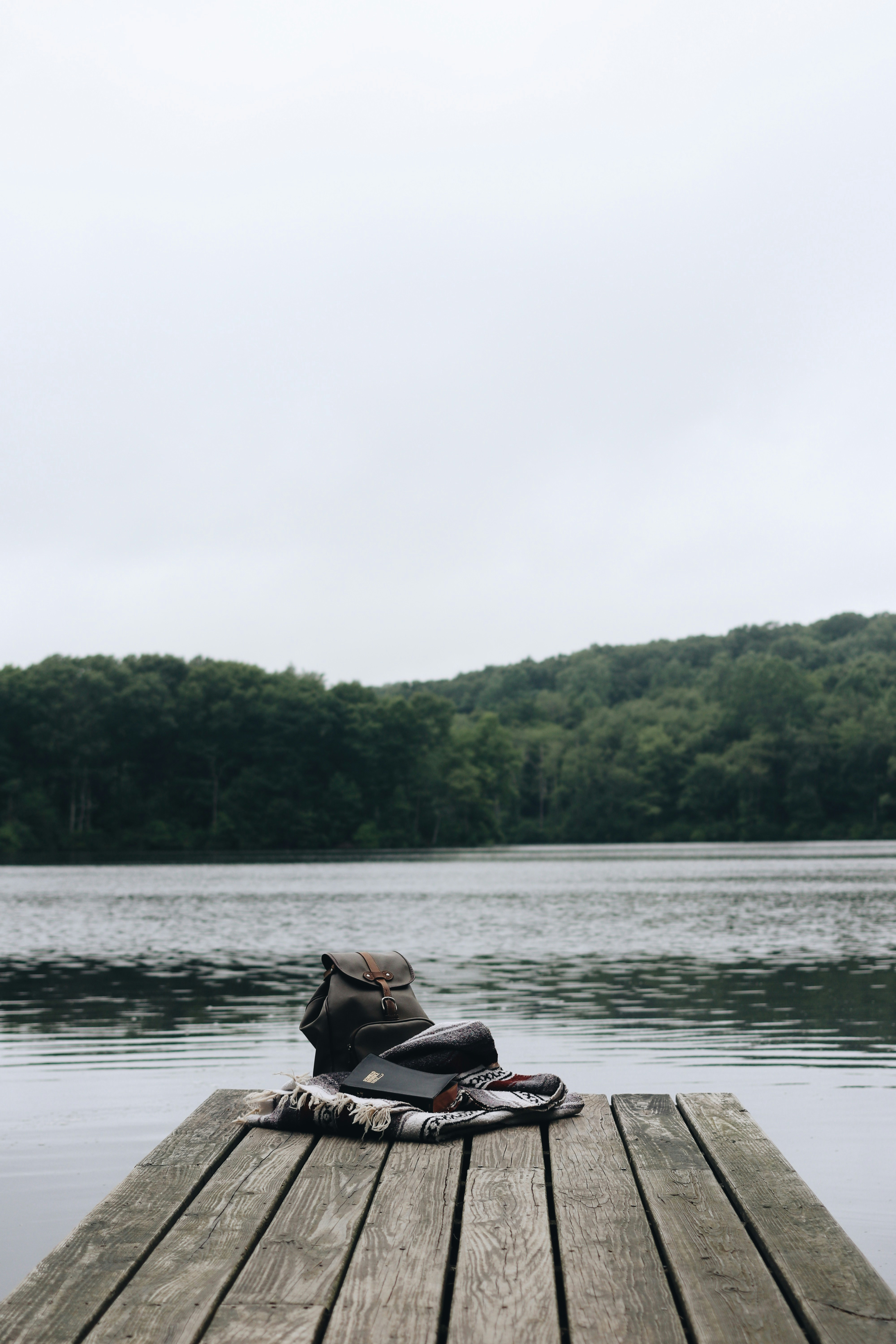 A rustic hat and blanket resting on a wooden dock, overlooking a tranquil lake surrounded by lush greenery.