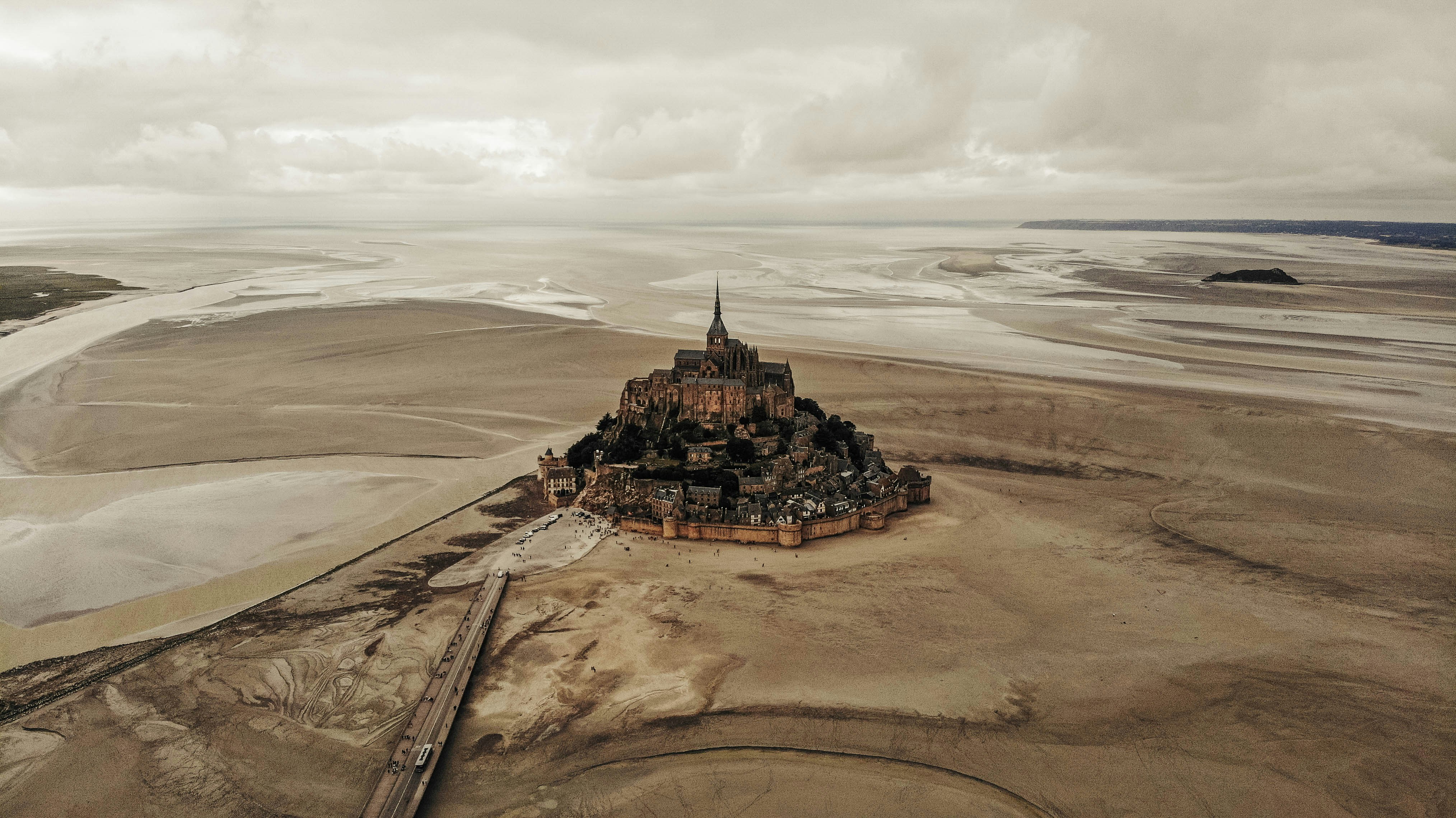 Aerial view of Mont Saint-Michel, a historic island commune, surrounded by vast tidal flats under a moody sky.