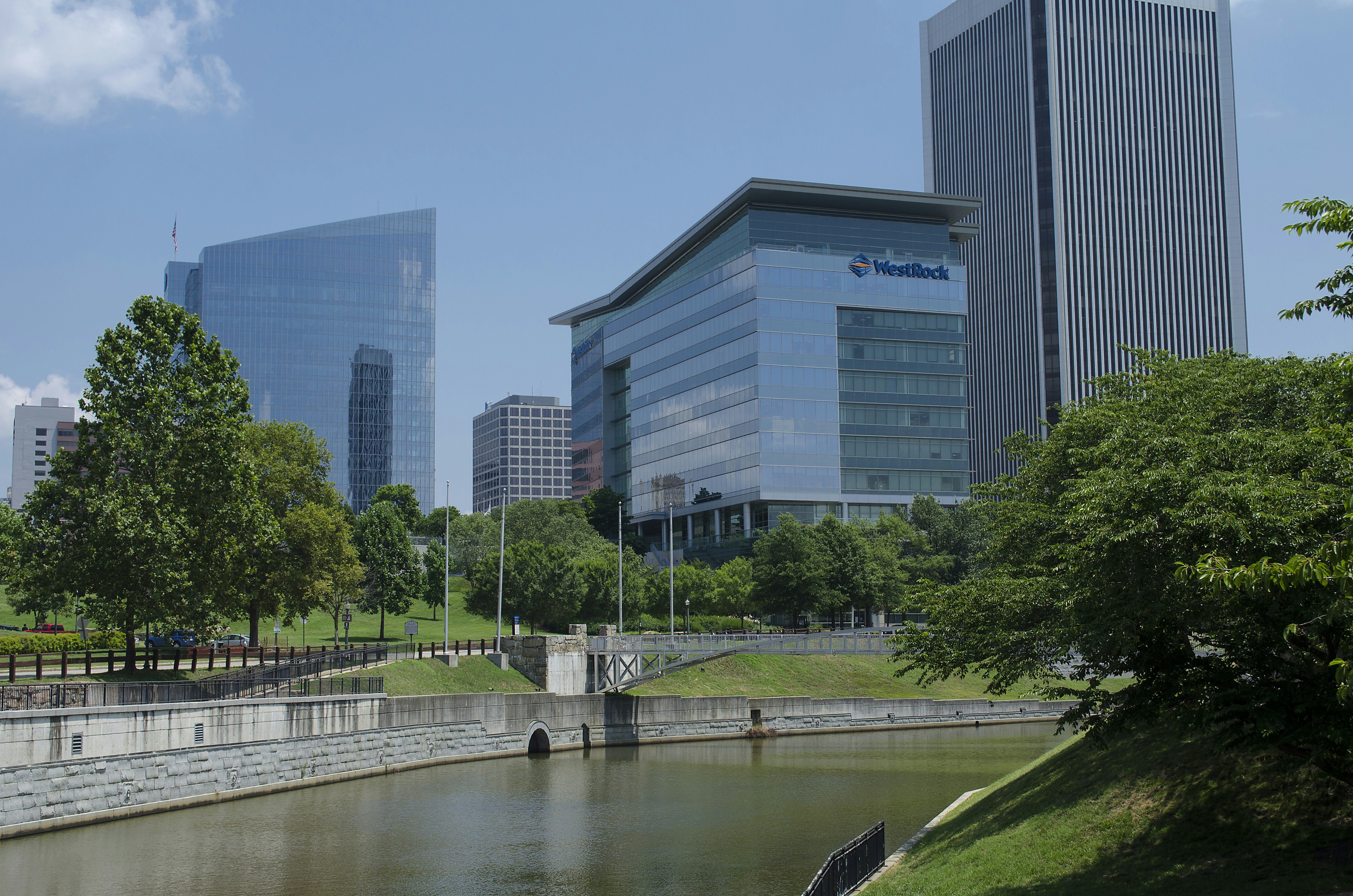 Modern buildings overlooking a tranquil canal surrounded by lush greenery under a clear blue sky.