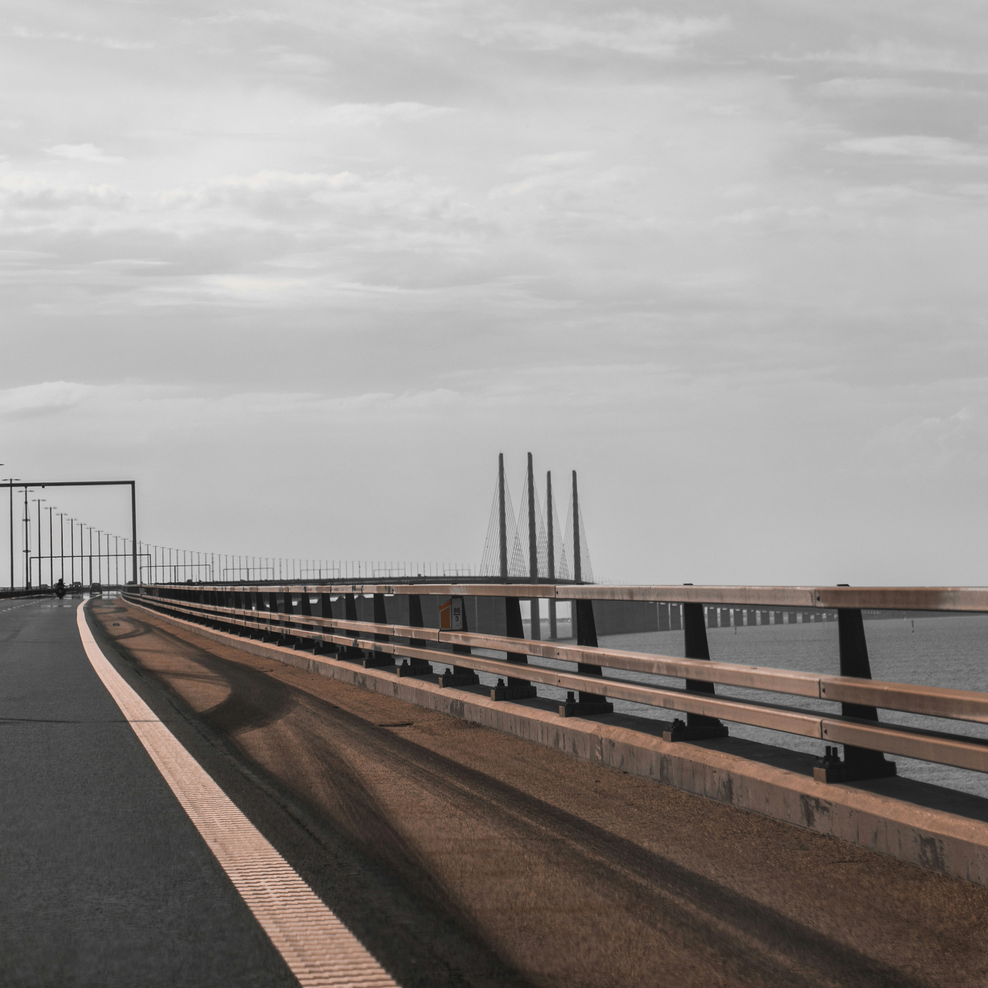 Curved roadway leading towards a distant bridge, framed by a cloudy sky. The composition emphasizes the journey and architectural design.
