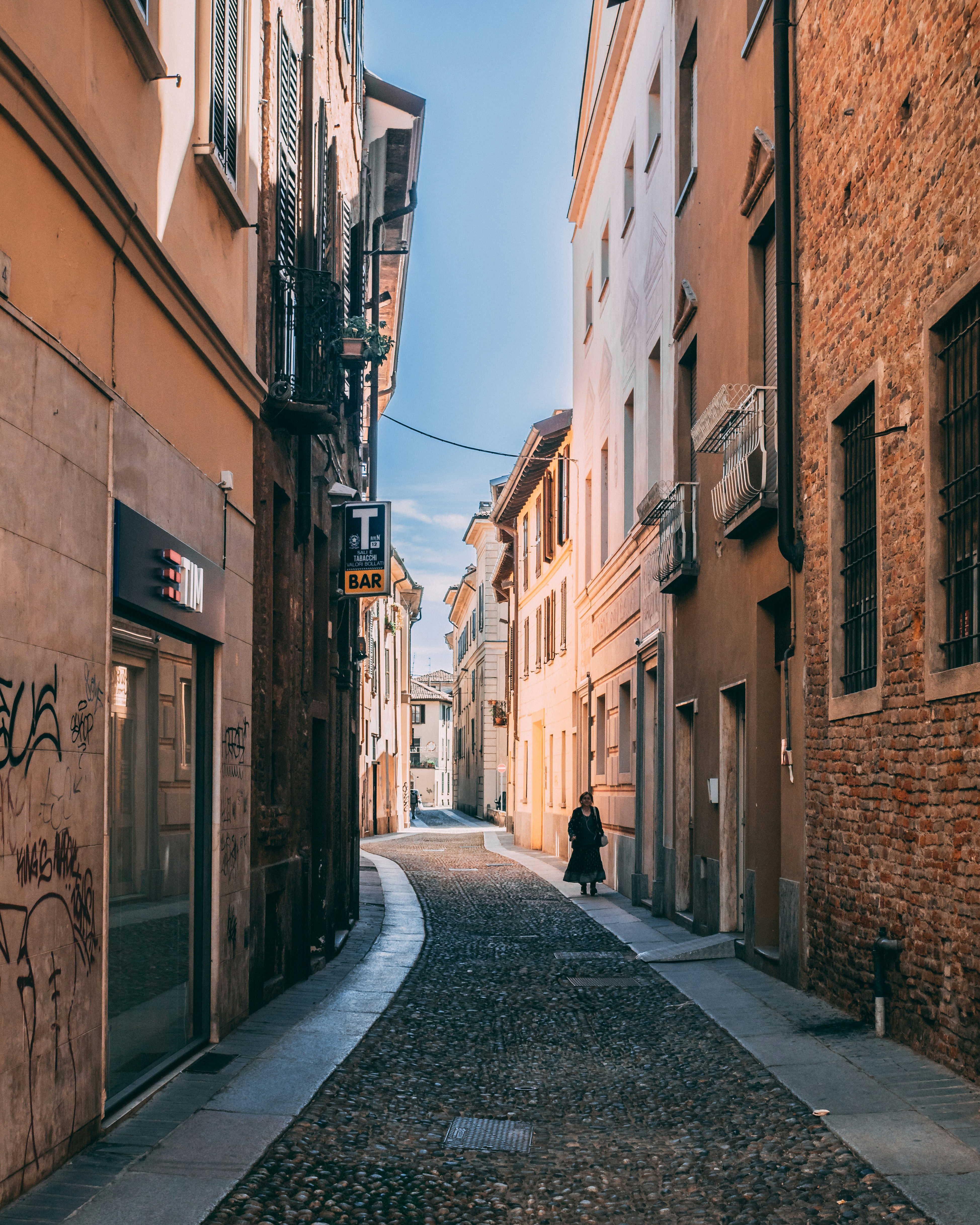 Narrow cobblestone street lined with aged buildings under a clear blue sky.