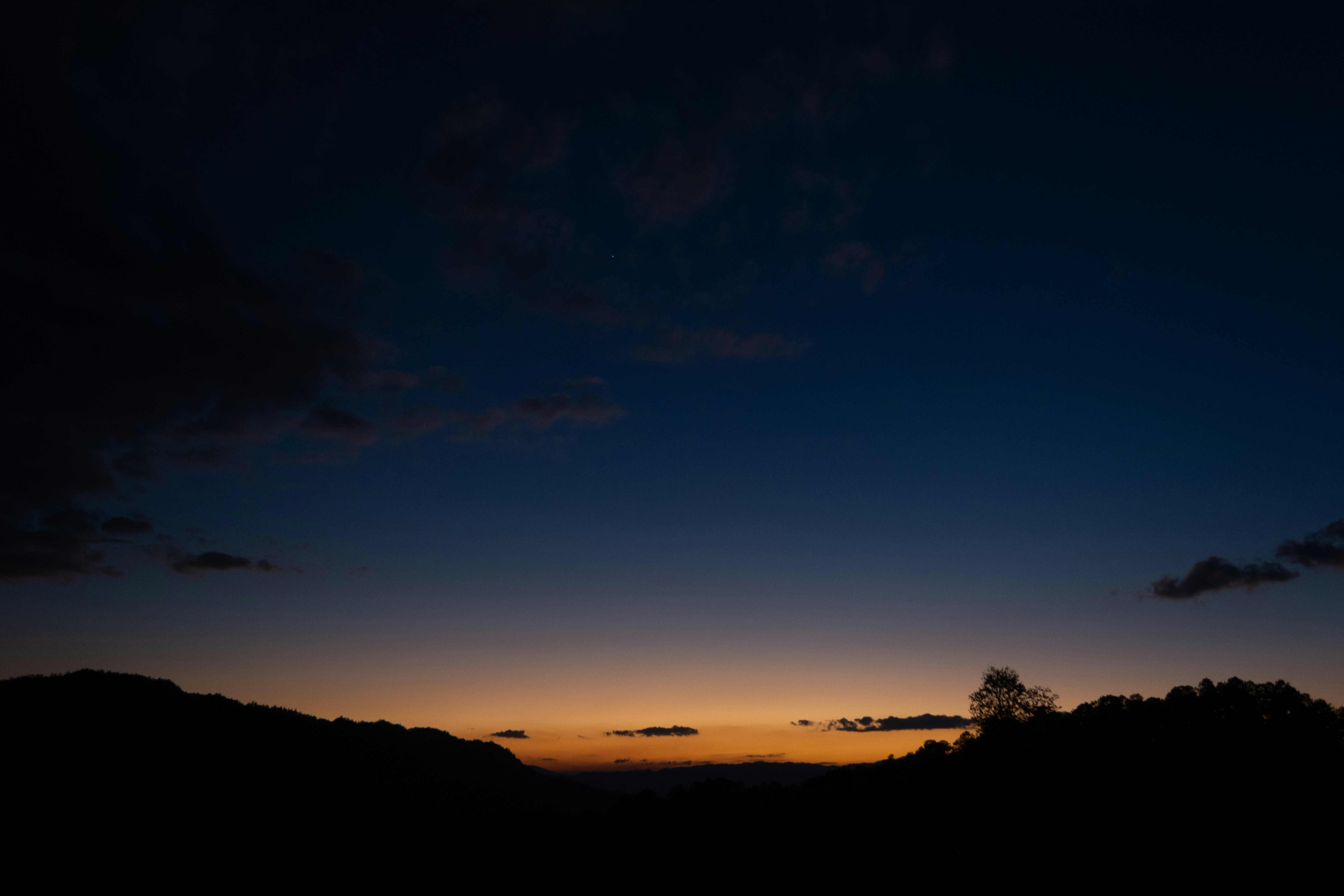 Silhouette of hills against a vibrant twilight sky transitioning from orange to deep blue.