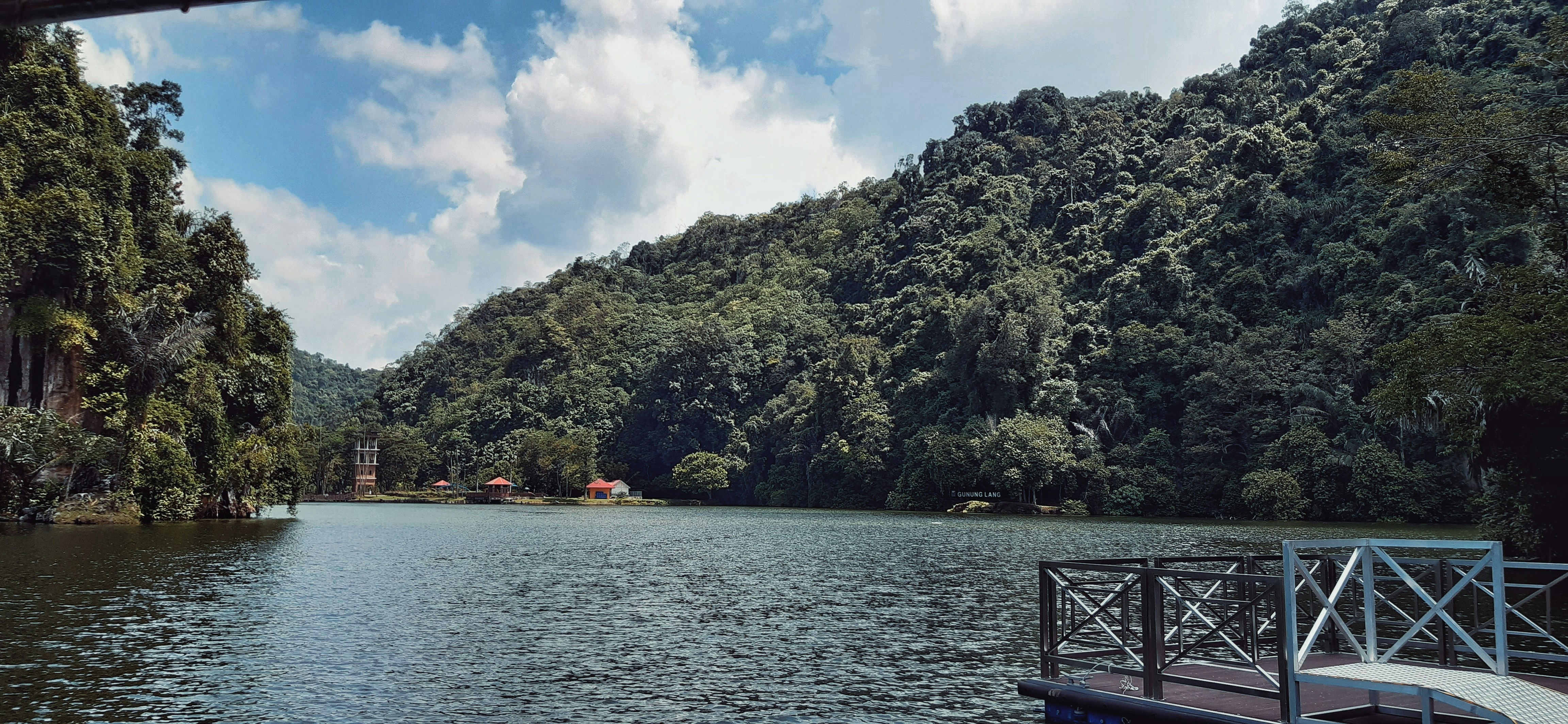 Tranquil lake bordered by lush green hills and a wooden dock under a partly cloudy sky.