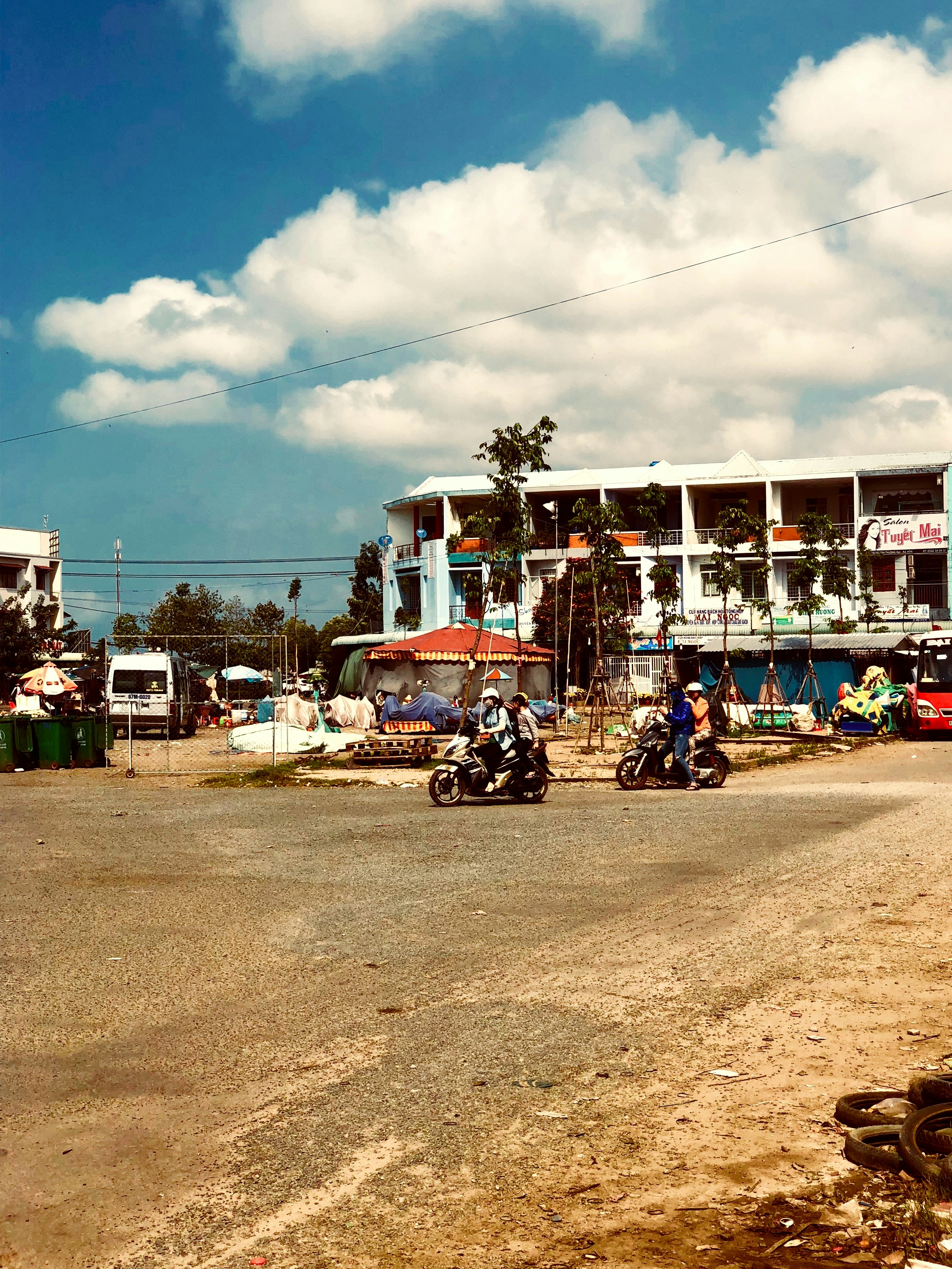 Market Corridor in Motion: Two Motorbikes Thread Through a Bustling Street