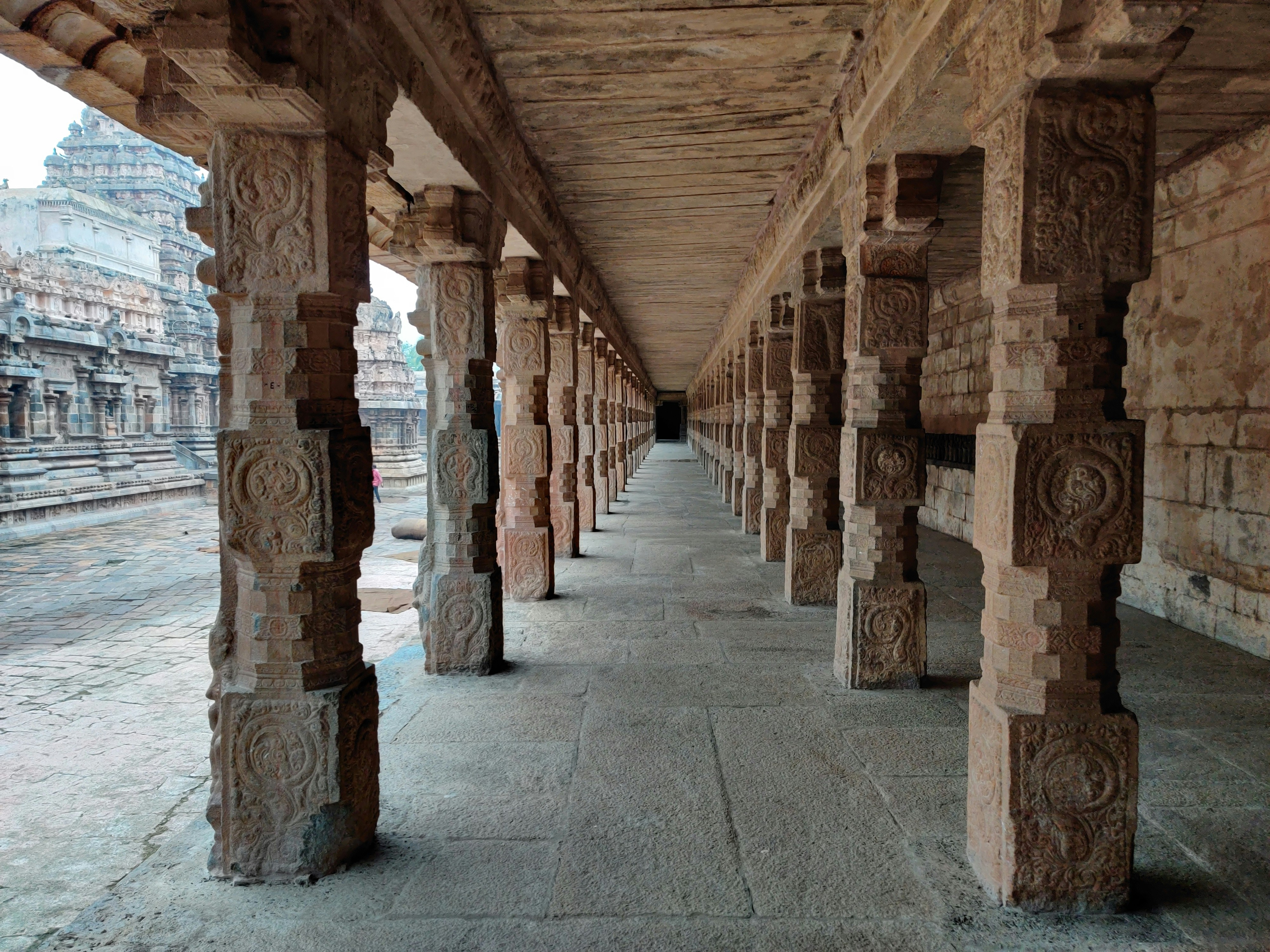 Intricate stone pillars line a historic corridor, leading towards a distant temple structure in the background.
