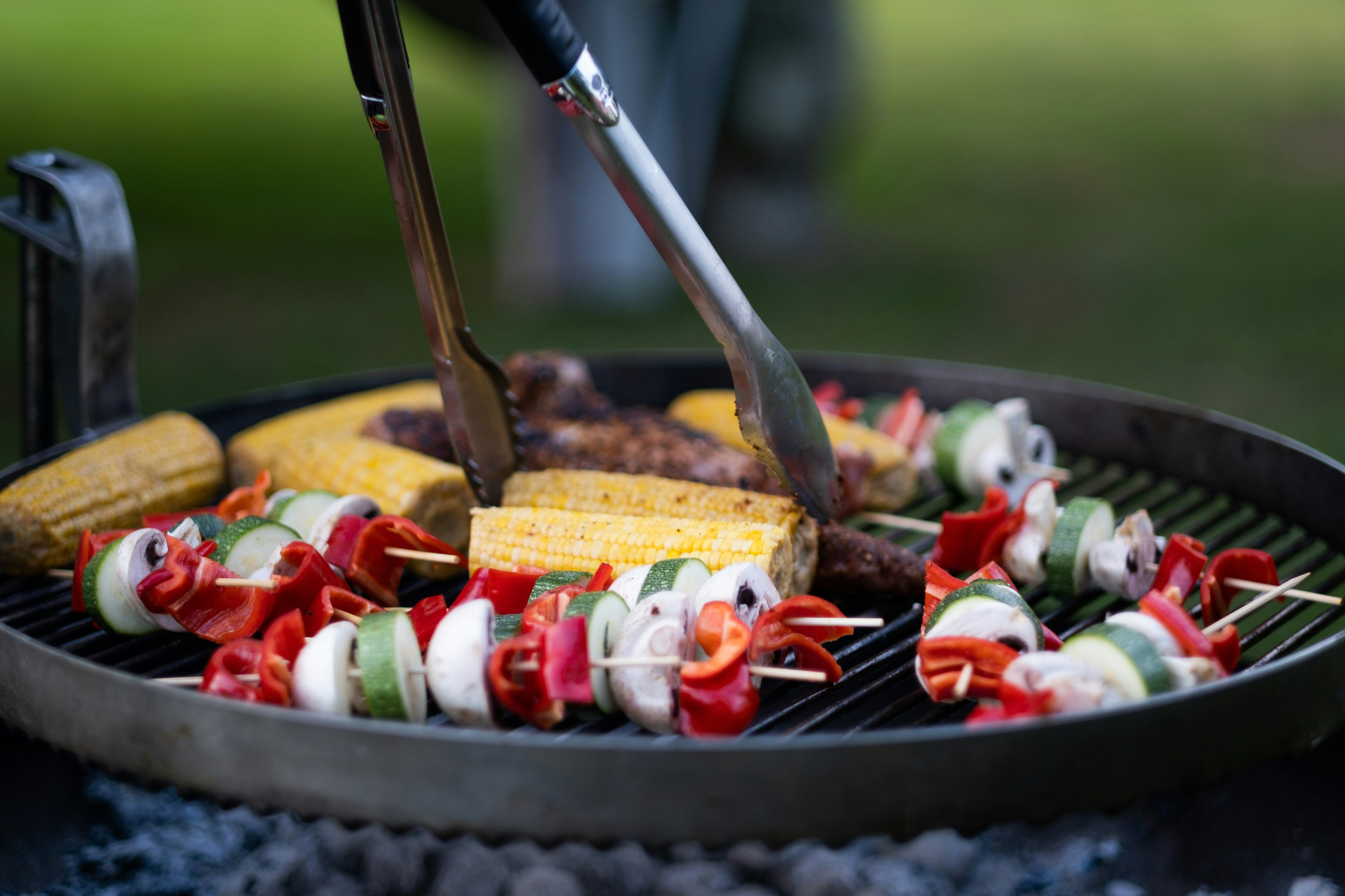 Colorful skewers of vegetables and meat alongside golden corn on a grill, showcasing a vibrant outdoor cooking scene.