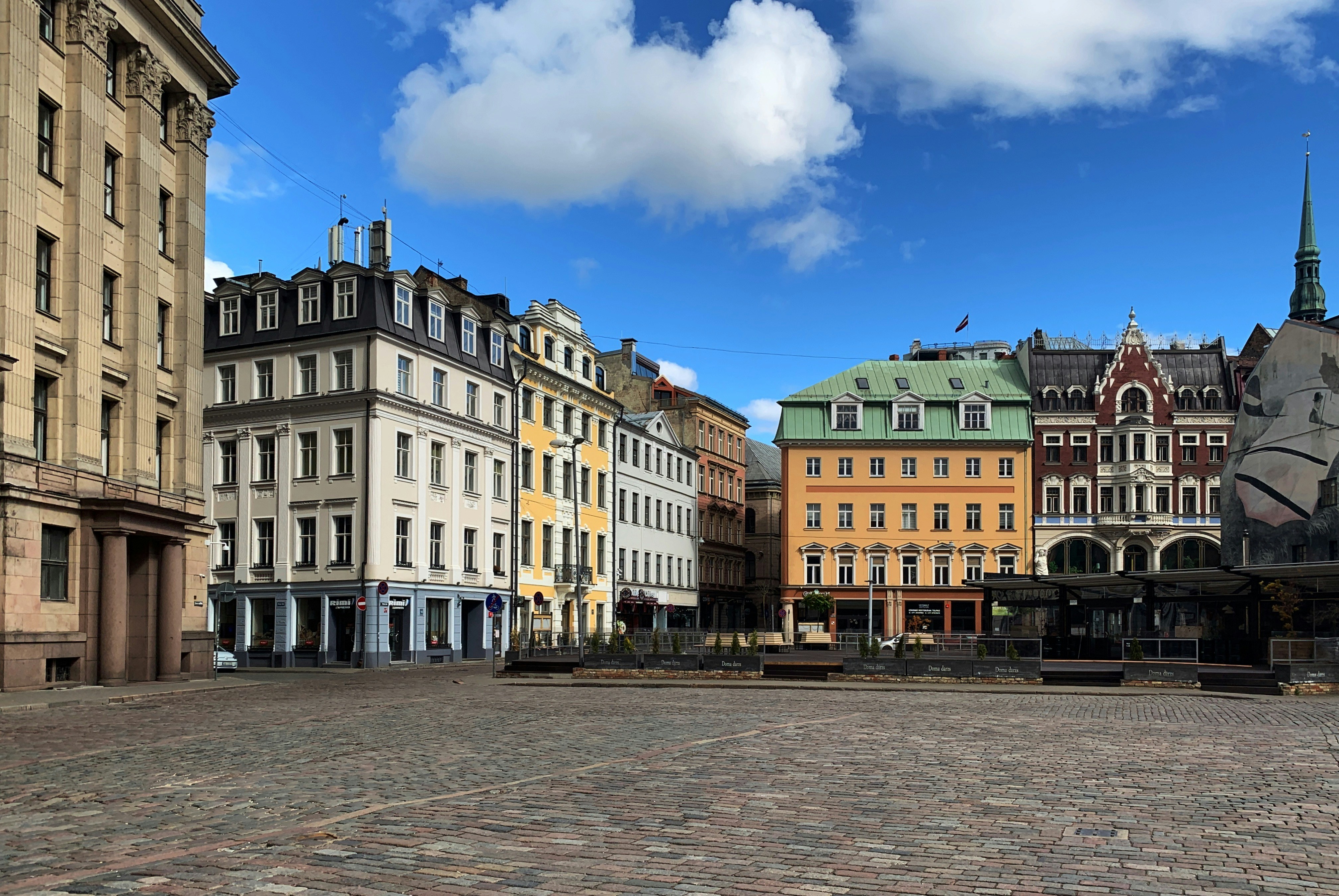 Colorful historic buildings line an open cobblestone square beneath a bright blue sky with fluffy clouds.