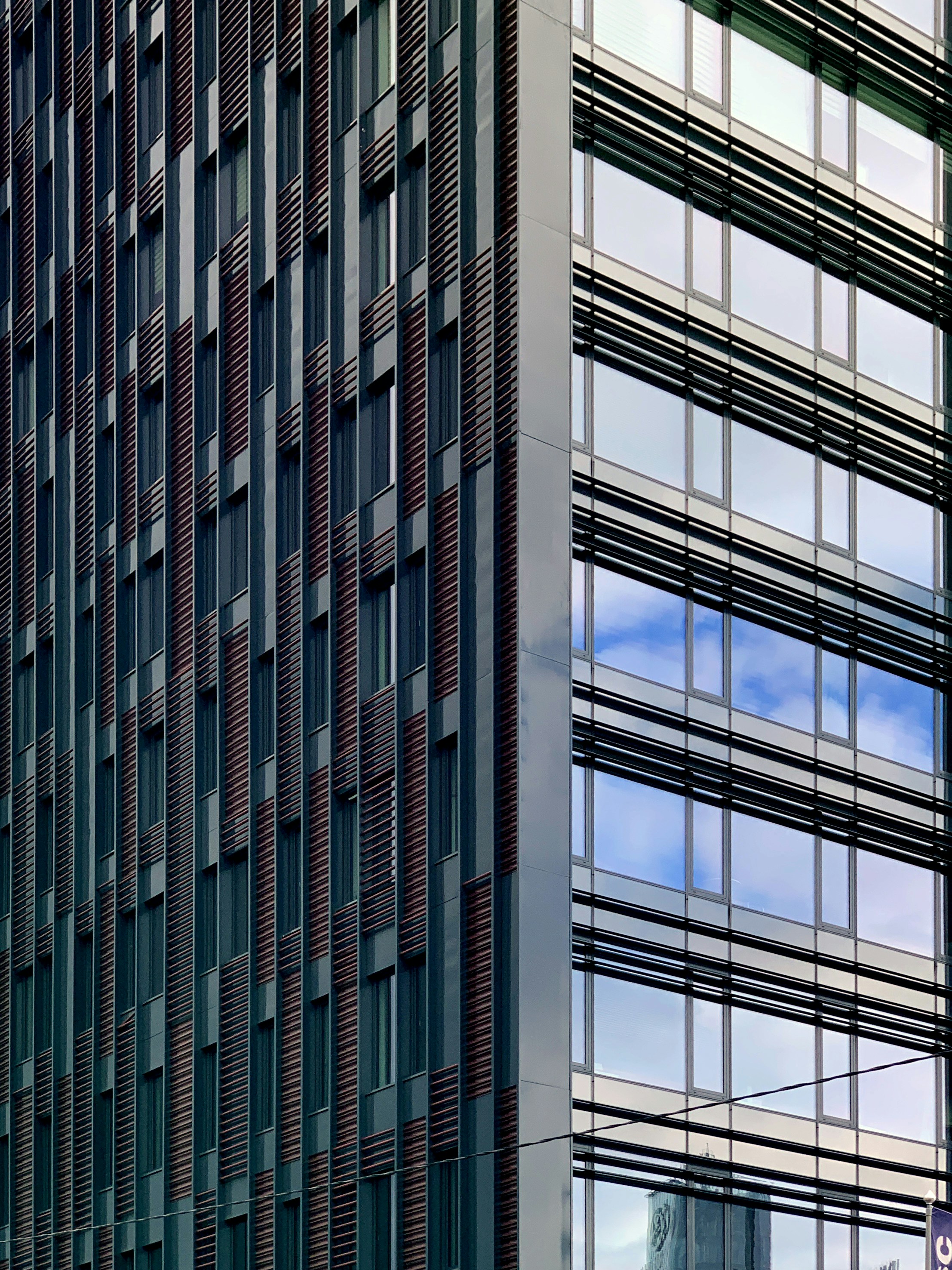 Close-up of a modern building facade showcasing a blend of textured panels and reflective glass. The interplay of materials highlights contemporary architectural design.