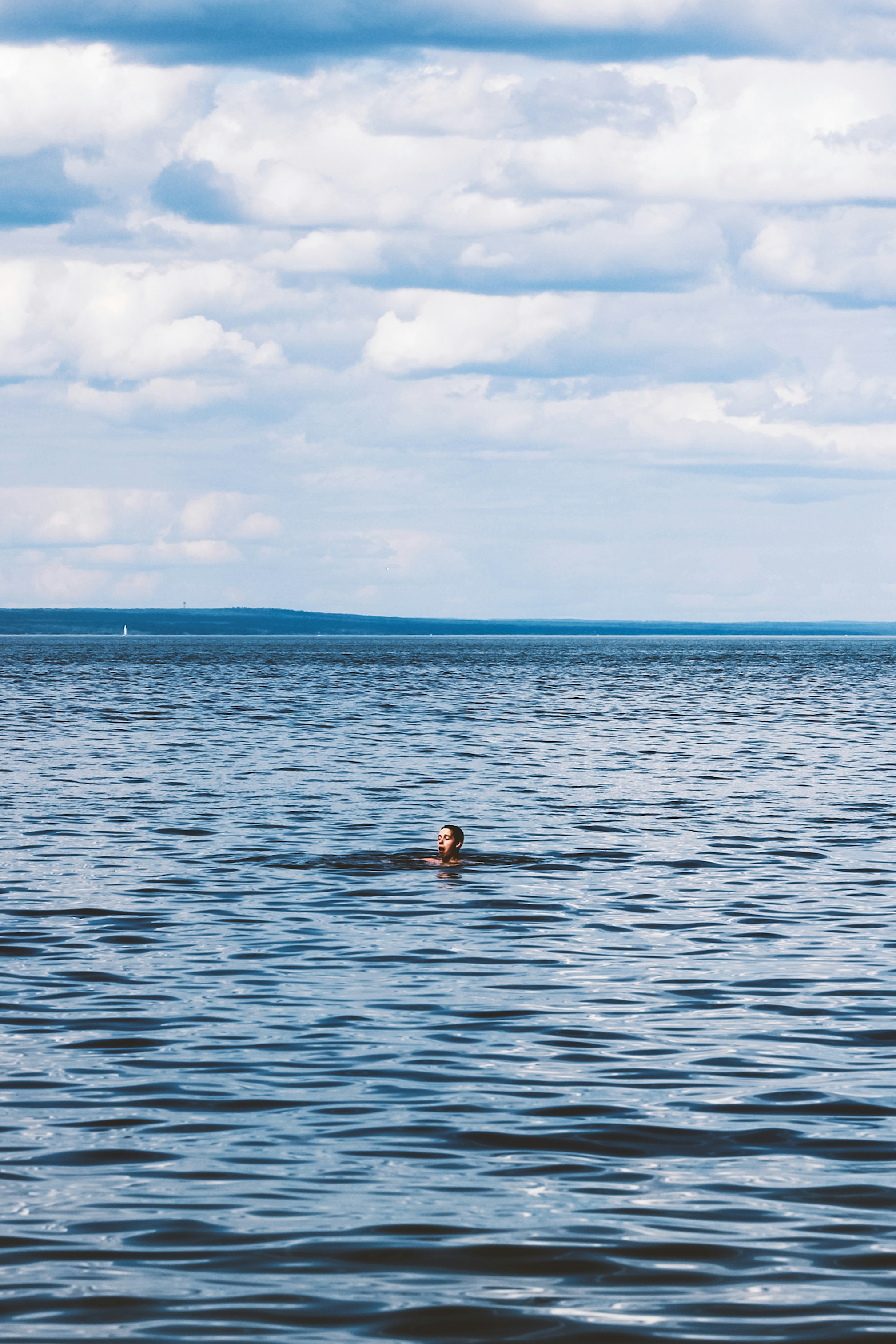 Solitary Swimmer Drifts Across a Calm Lake Under a Cloud-Swept Sky