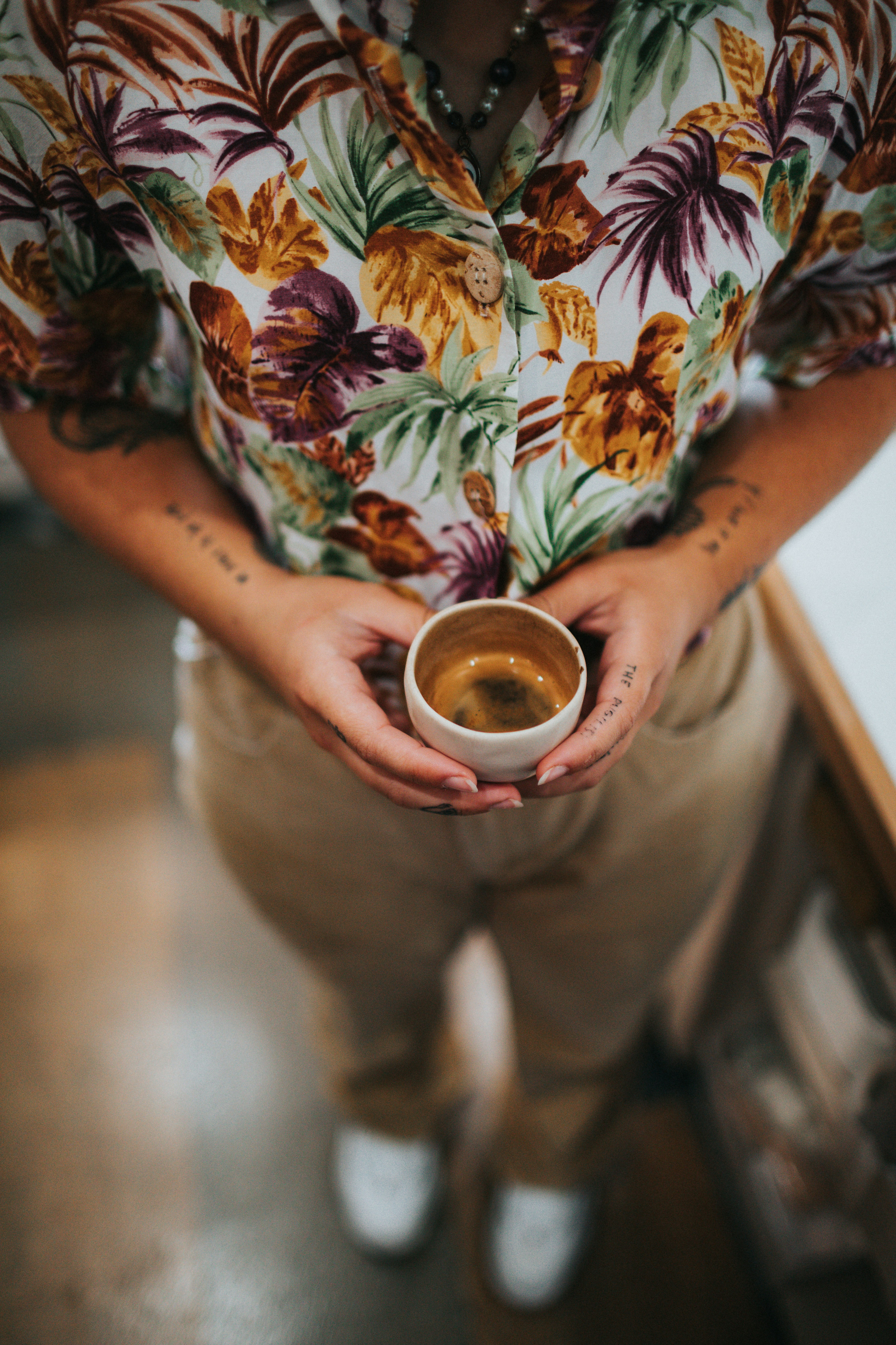 Individual holding a small cup of coffee, dressed in a vibrant floral shirt, showcasing a blend of personal style and everyday ritual.