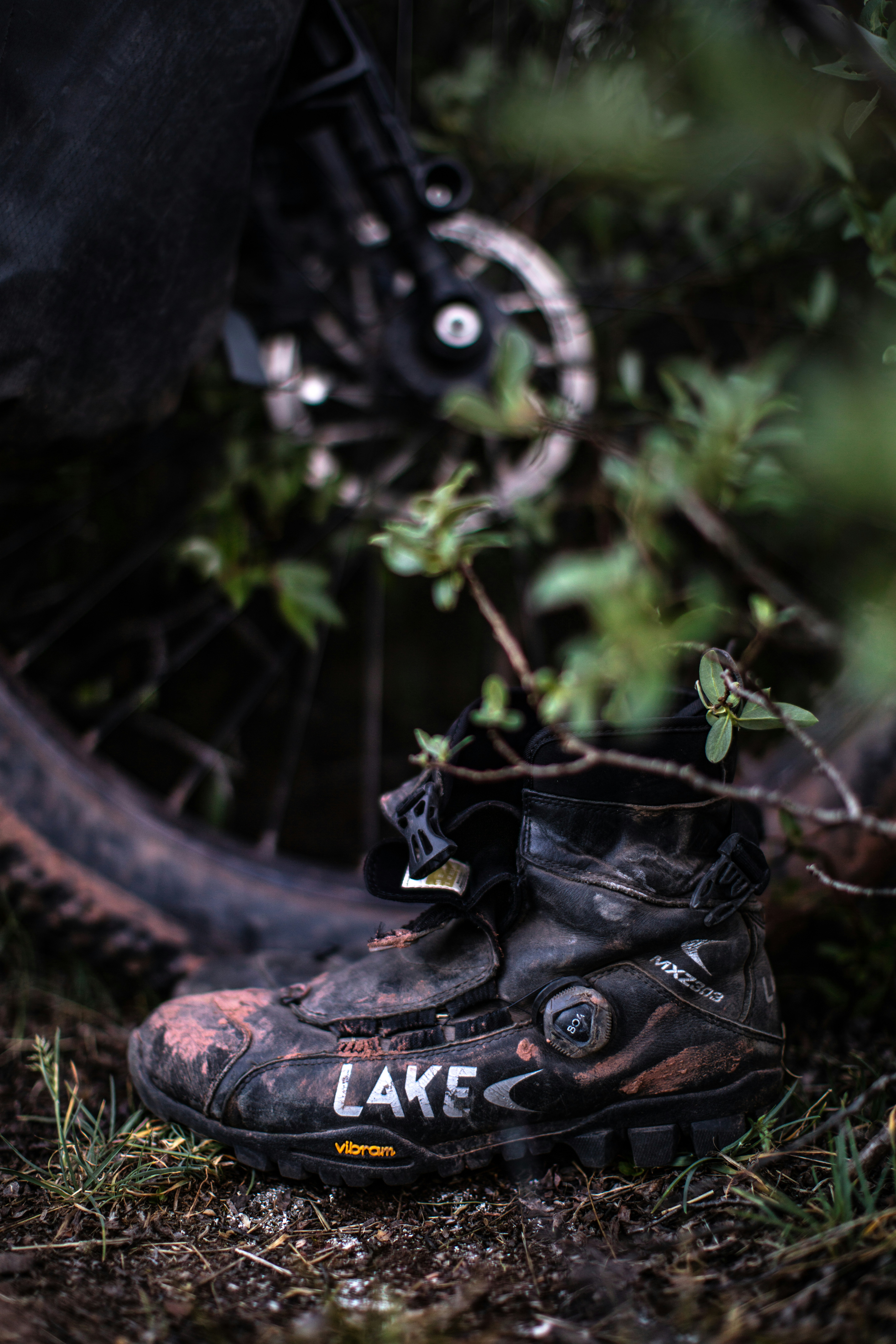Mud-Caked Trail Boot Pausing by a Worn Wheel