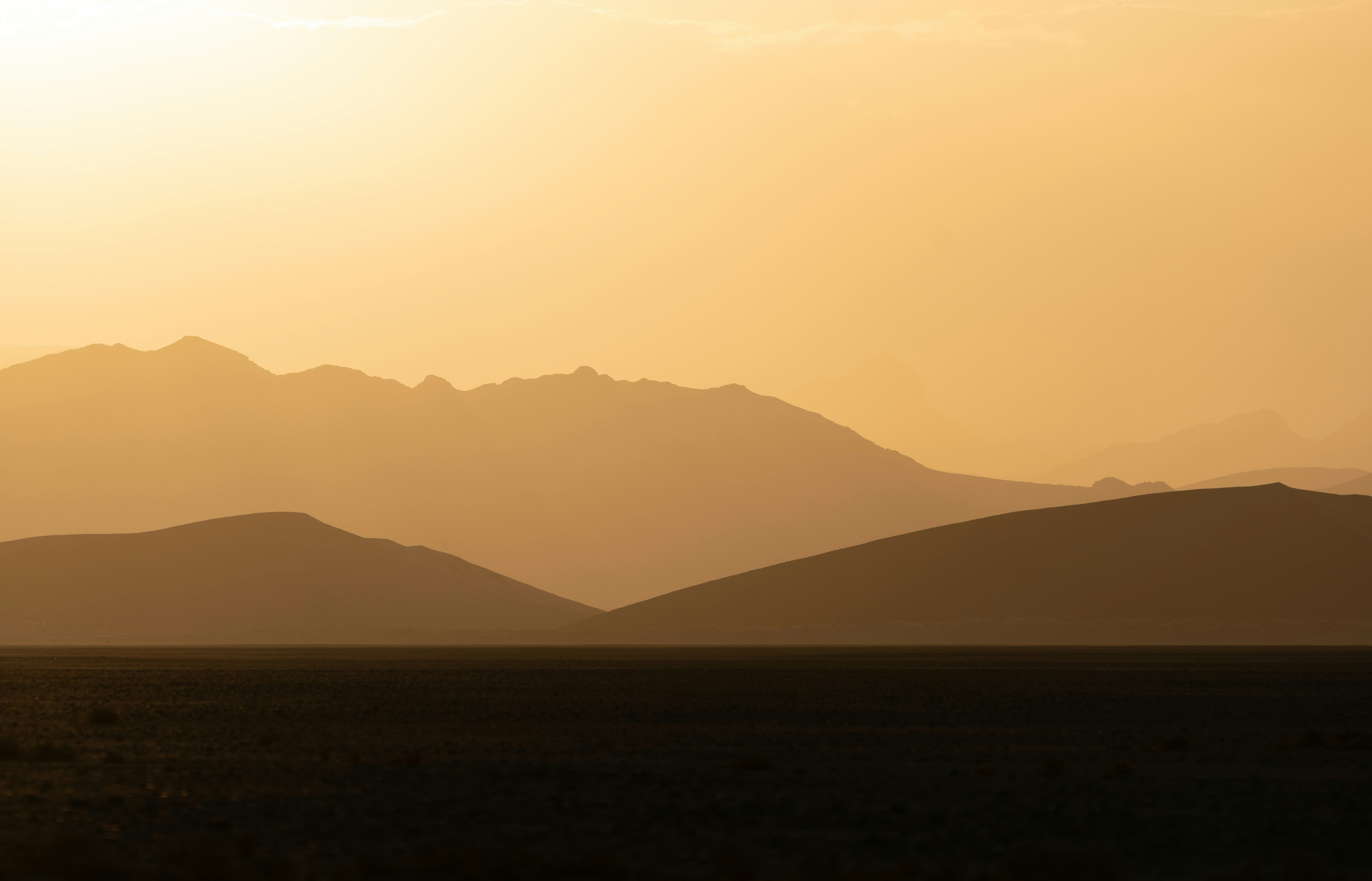 Silhouetted mountain ranges blend into a soft golden sky at twilight, creating a serene and tranquil landscape.