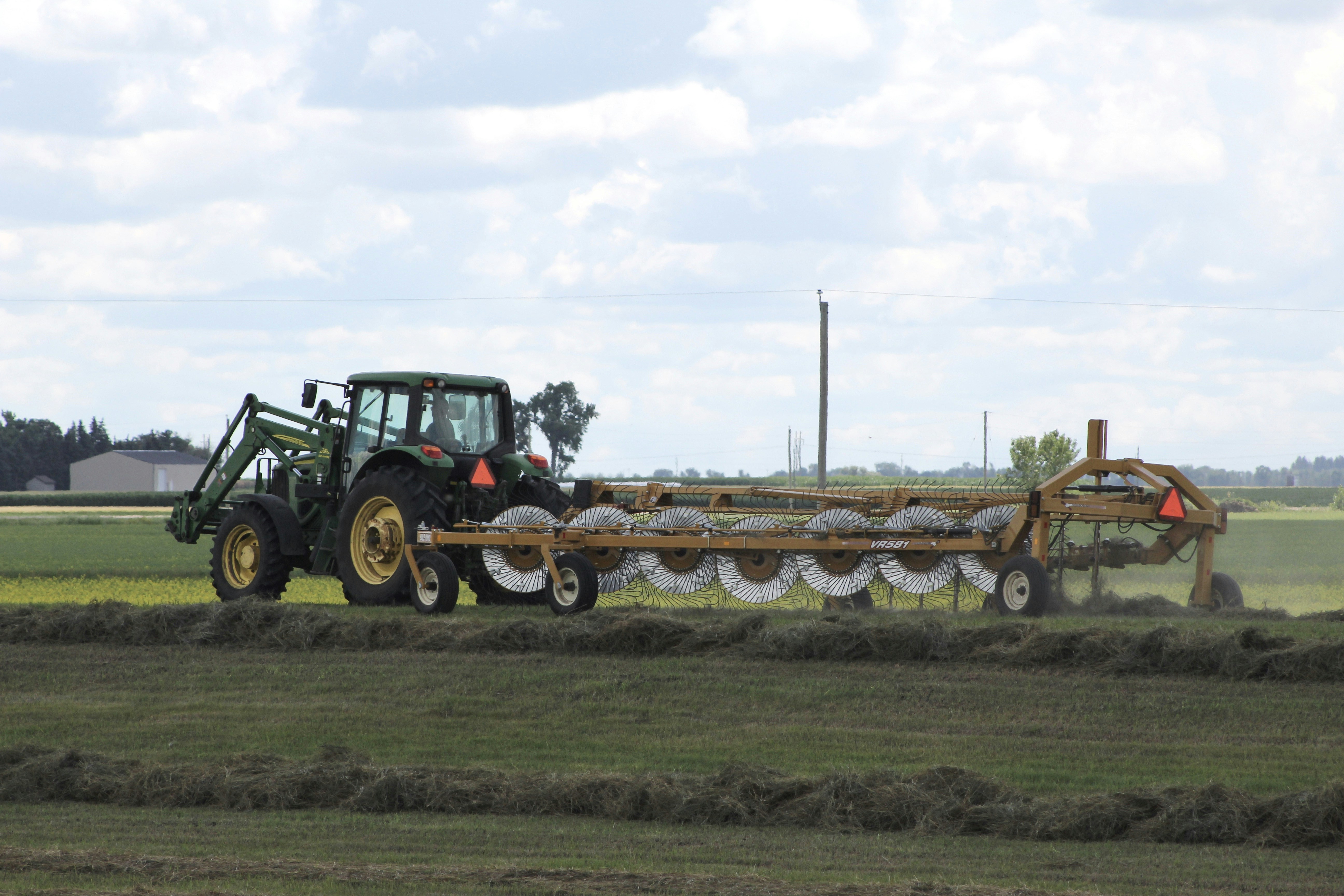 Line in the Field: Green Tractor Tows a Disc Harrow Under a Cloudy Sky
